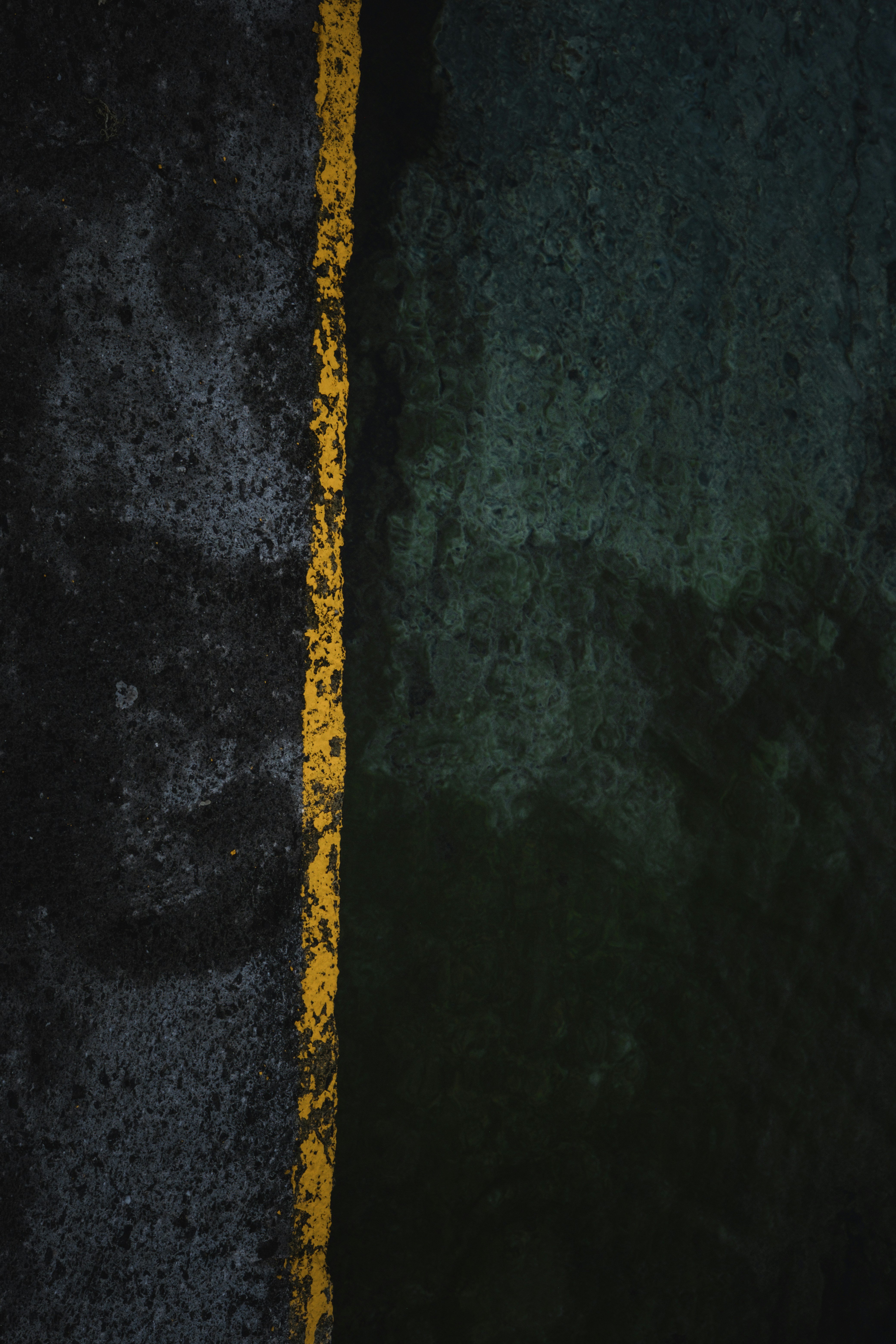 A close-up view of a yellow line contrasting against dark asphalt and tranquil water, highlighting the boundary between land and liquid.