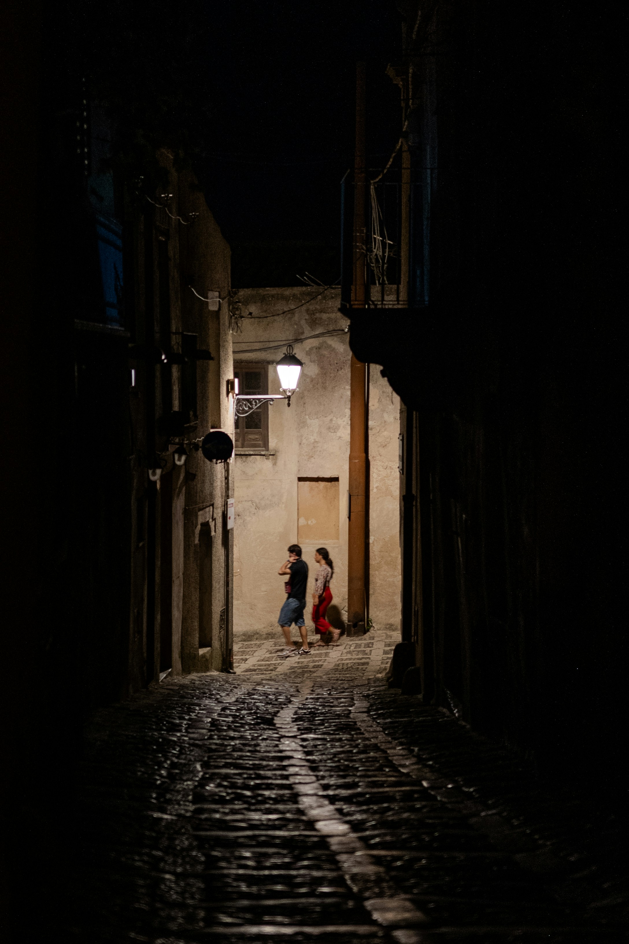 Couple walking down a dark cobblestone alley at night.