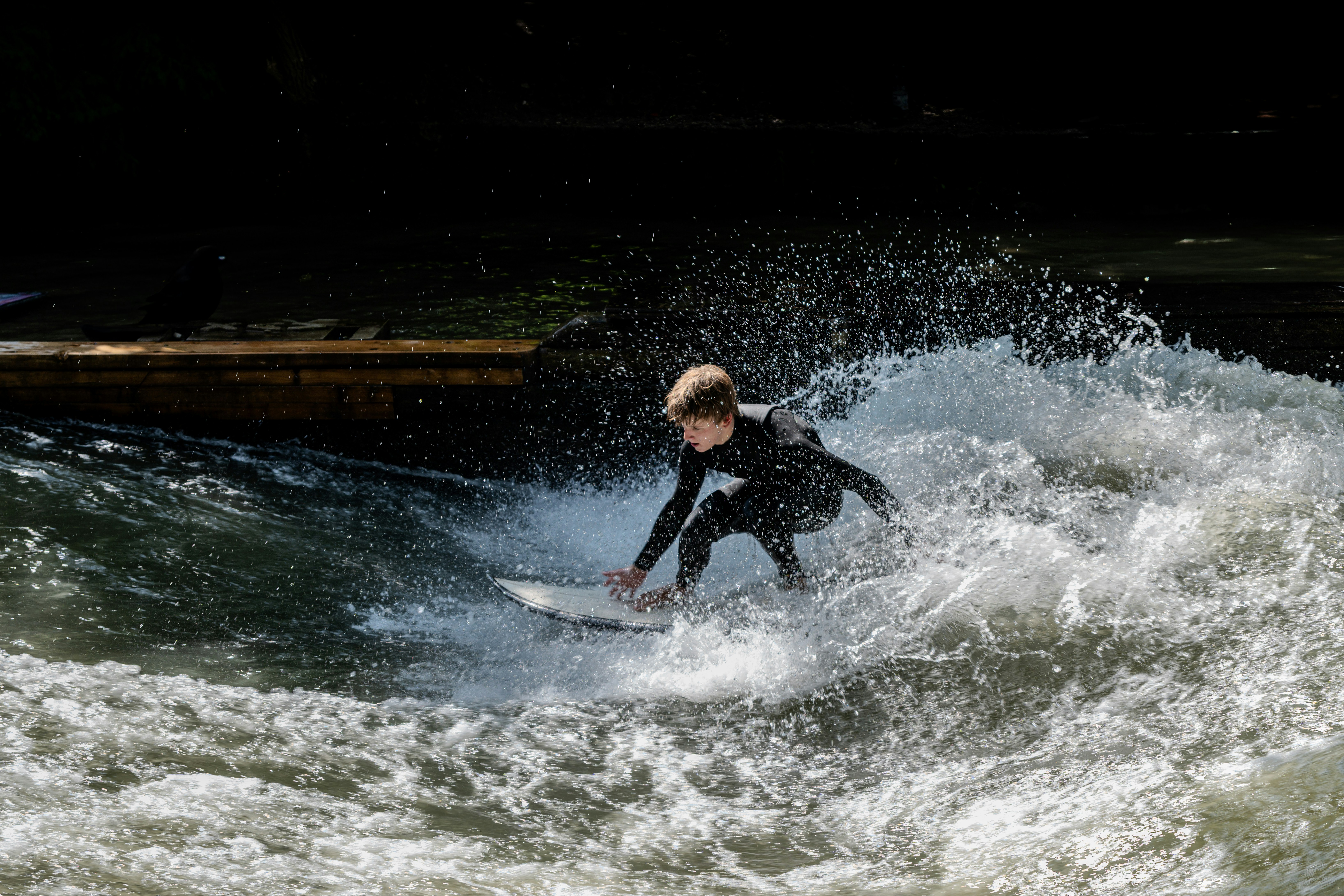 Surfer skillfully navigating a wave, creating a spray of water against a dark backdrop.