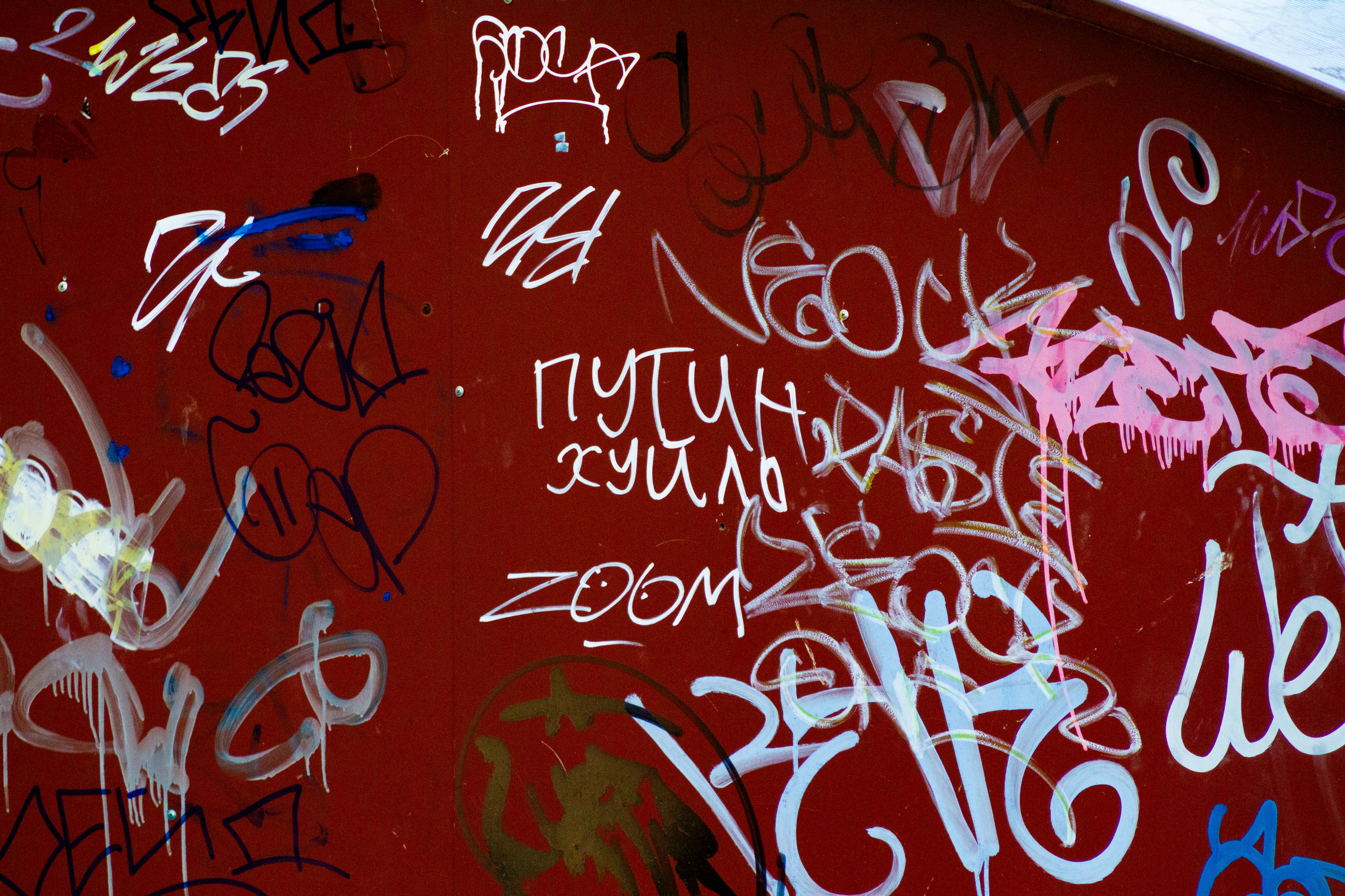 Red wall covered in diverse graffiti tags and spray paint tags