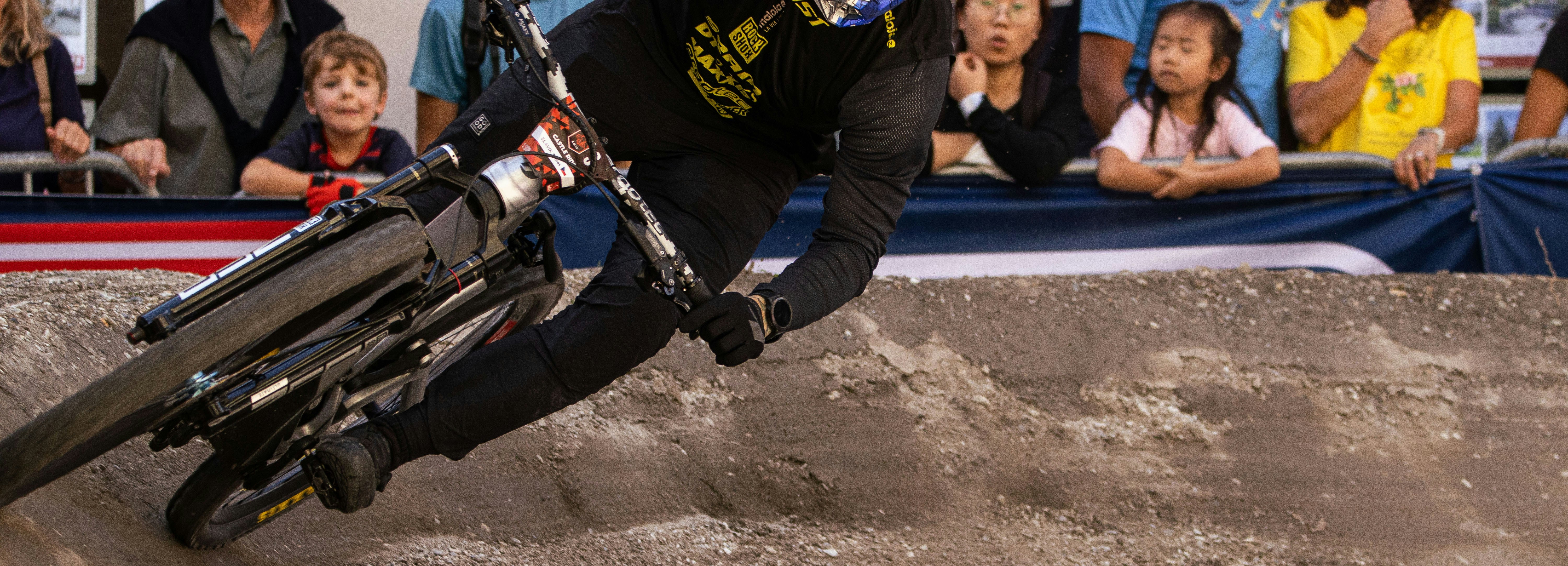 BMX rider executing a sharp turn on a dirt track, surrounded by an engaged audience. The scene captures the thrill of competitive cycling.