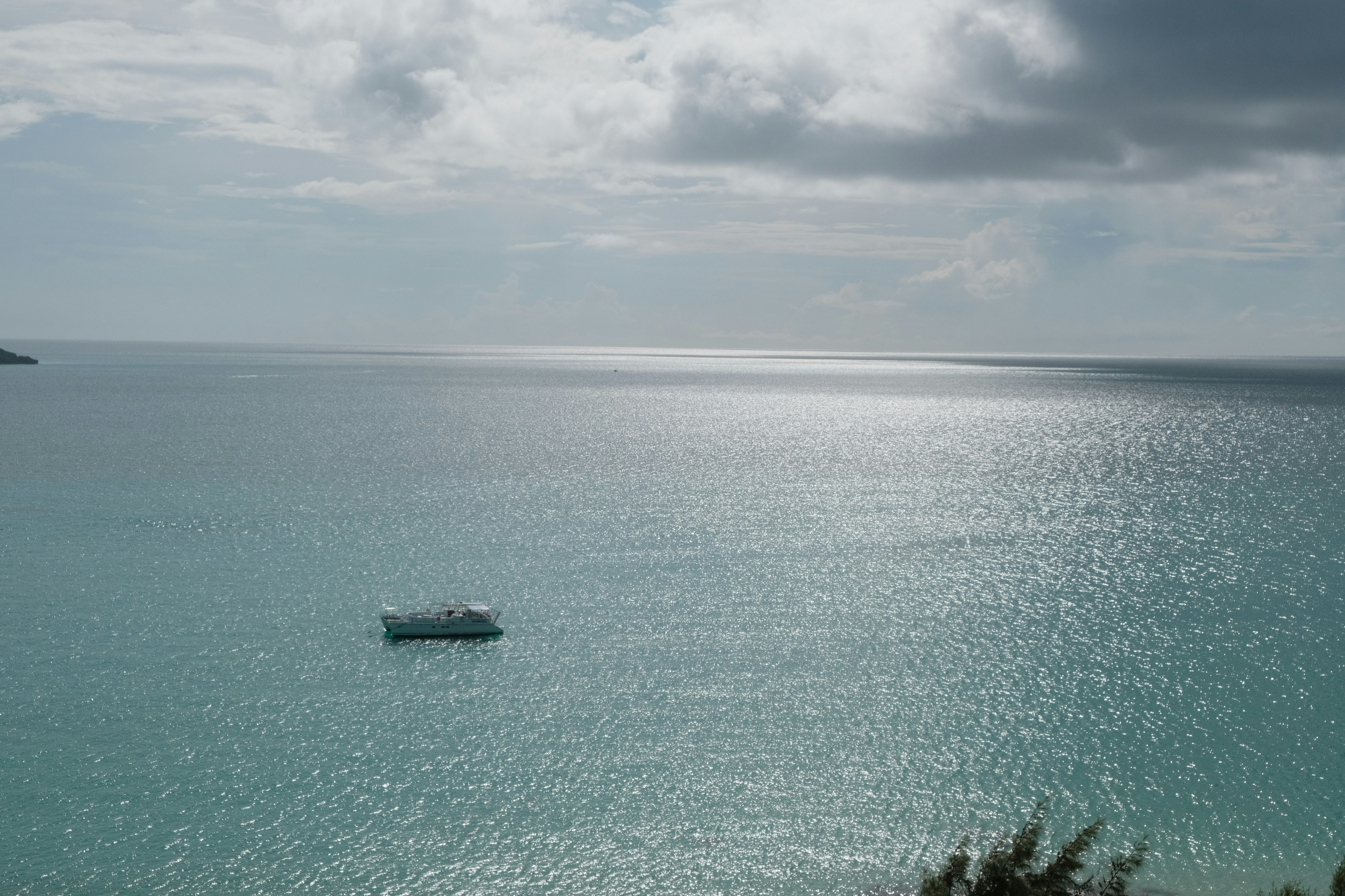 A tranquil seascape featuring a solitary boat gliding across the shimmering turquoise waters under a moody sky. The scene evokes a sense of calm and exploration.