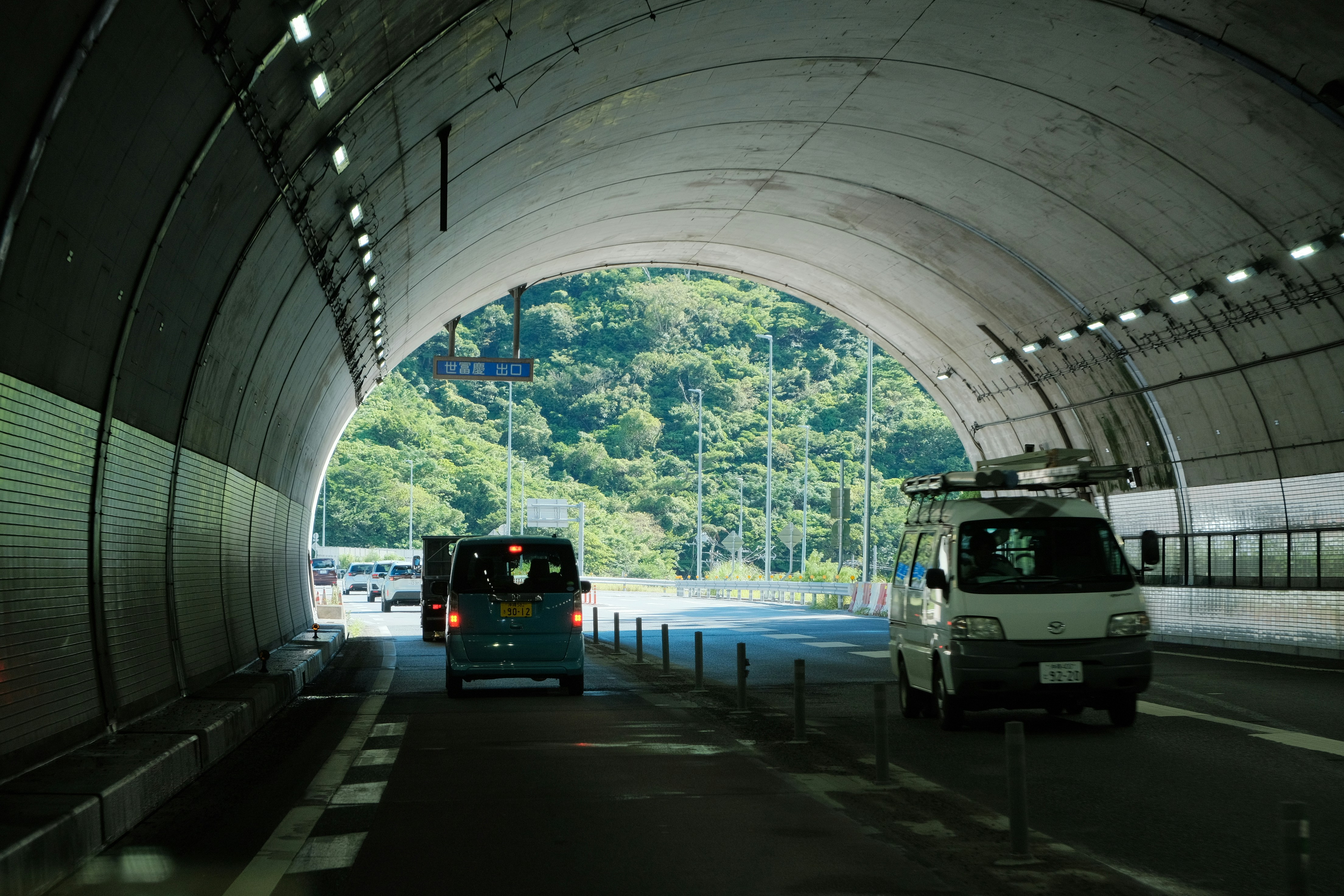 Vehicles driving through a brightly lit tunnel exit.