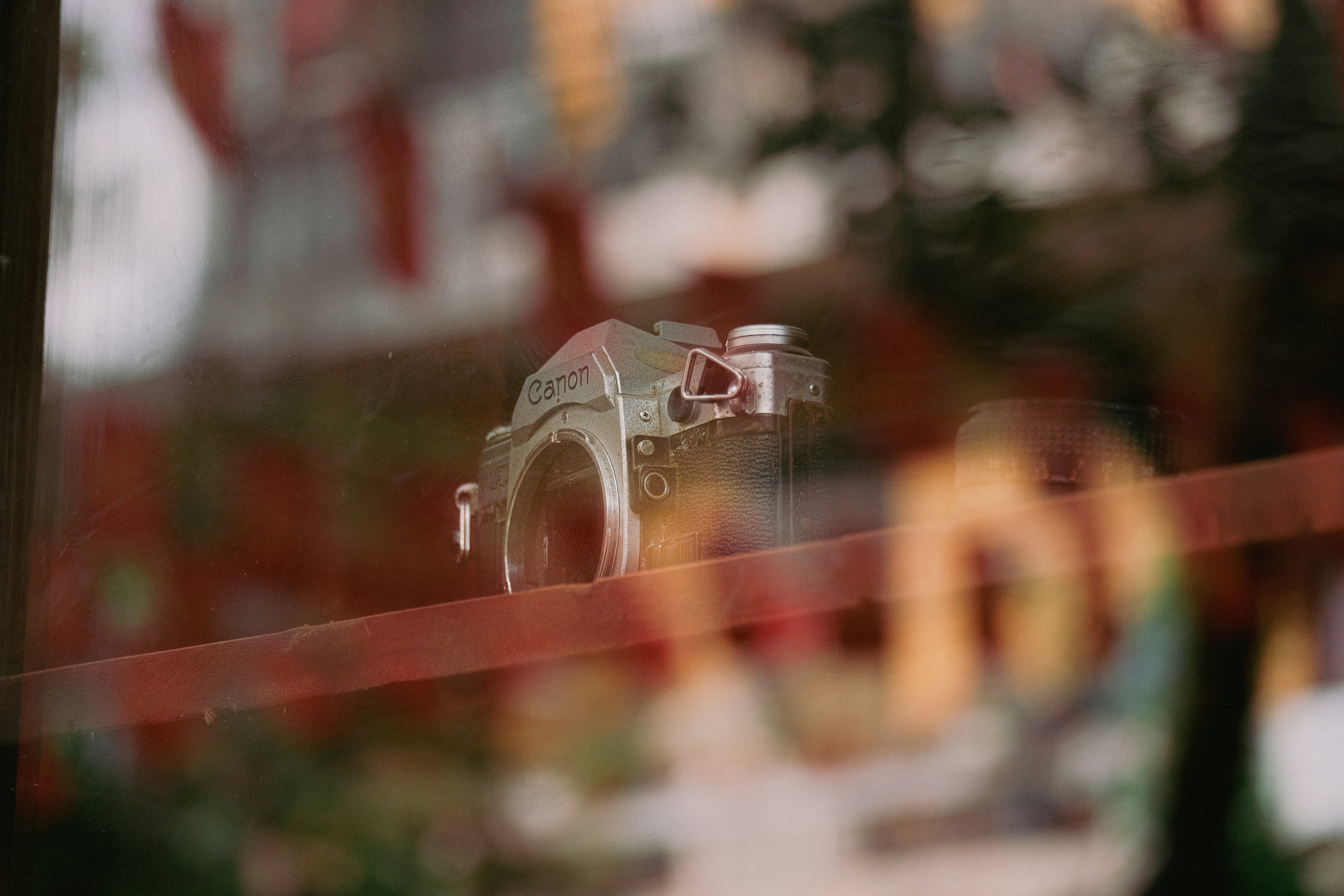 A vintage camera displayed in a shop window, reflecting the vibrant colors of the surroundings. The glass adds a layer of complexity to the scene.