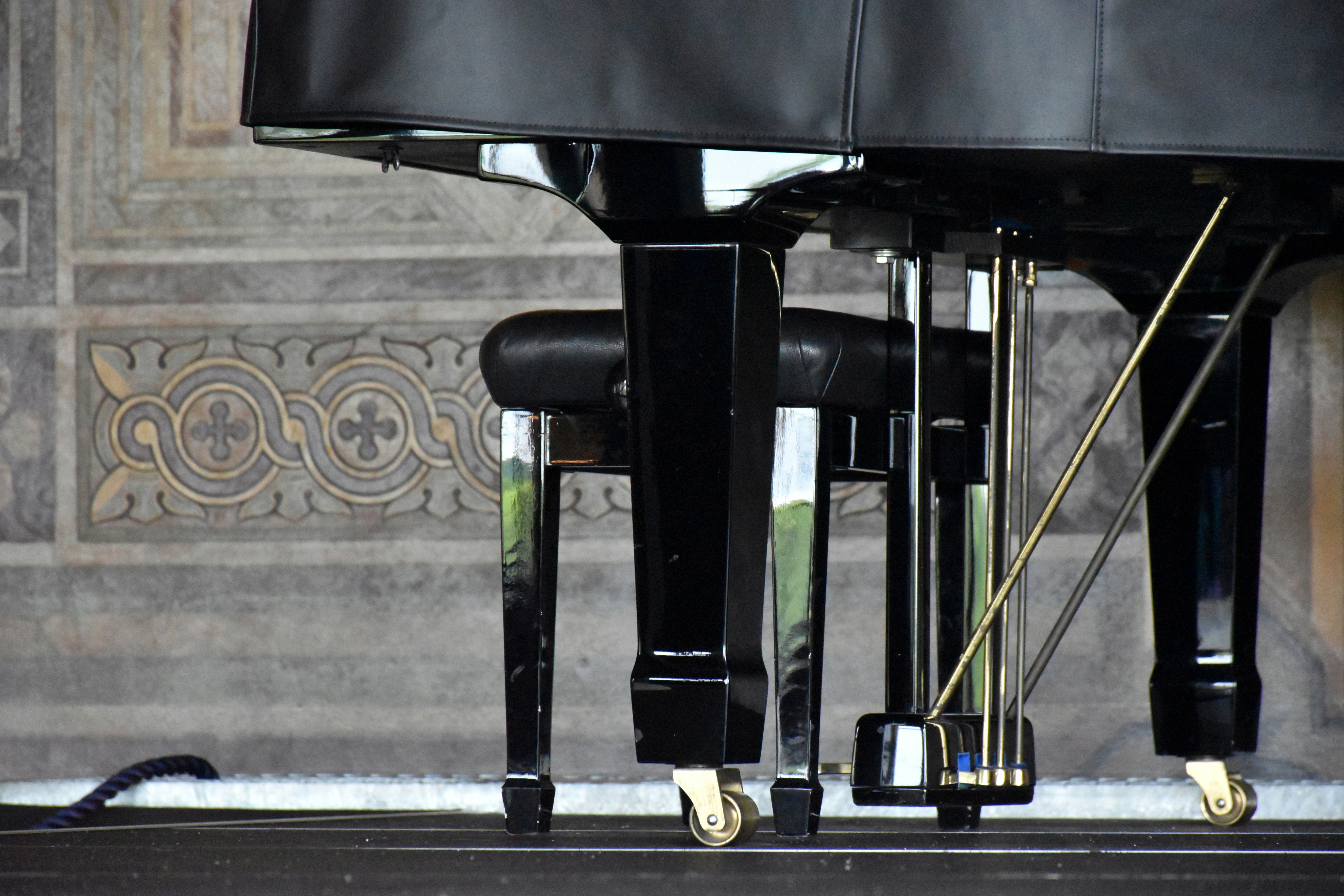 The undercarriage of a piano (Piano - music) | Black grand piano with a leather bench