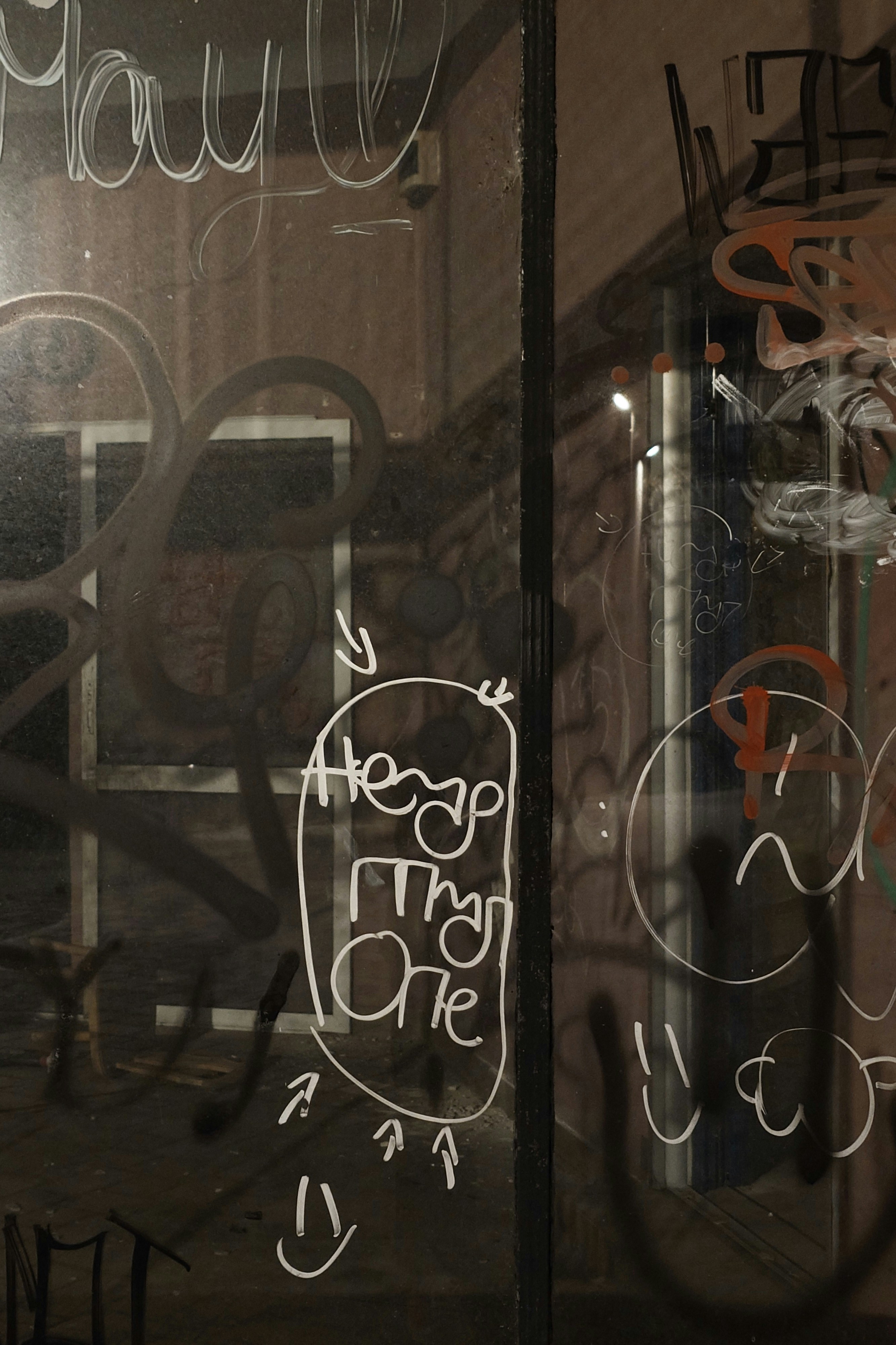 Layered graffiti on a glass surface, showcasing playful doodles and messages. The interplay of light and reflections adds depth to the urban landscape.