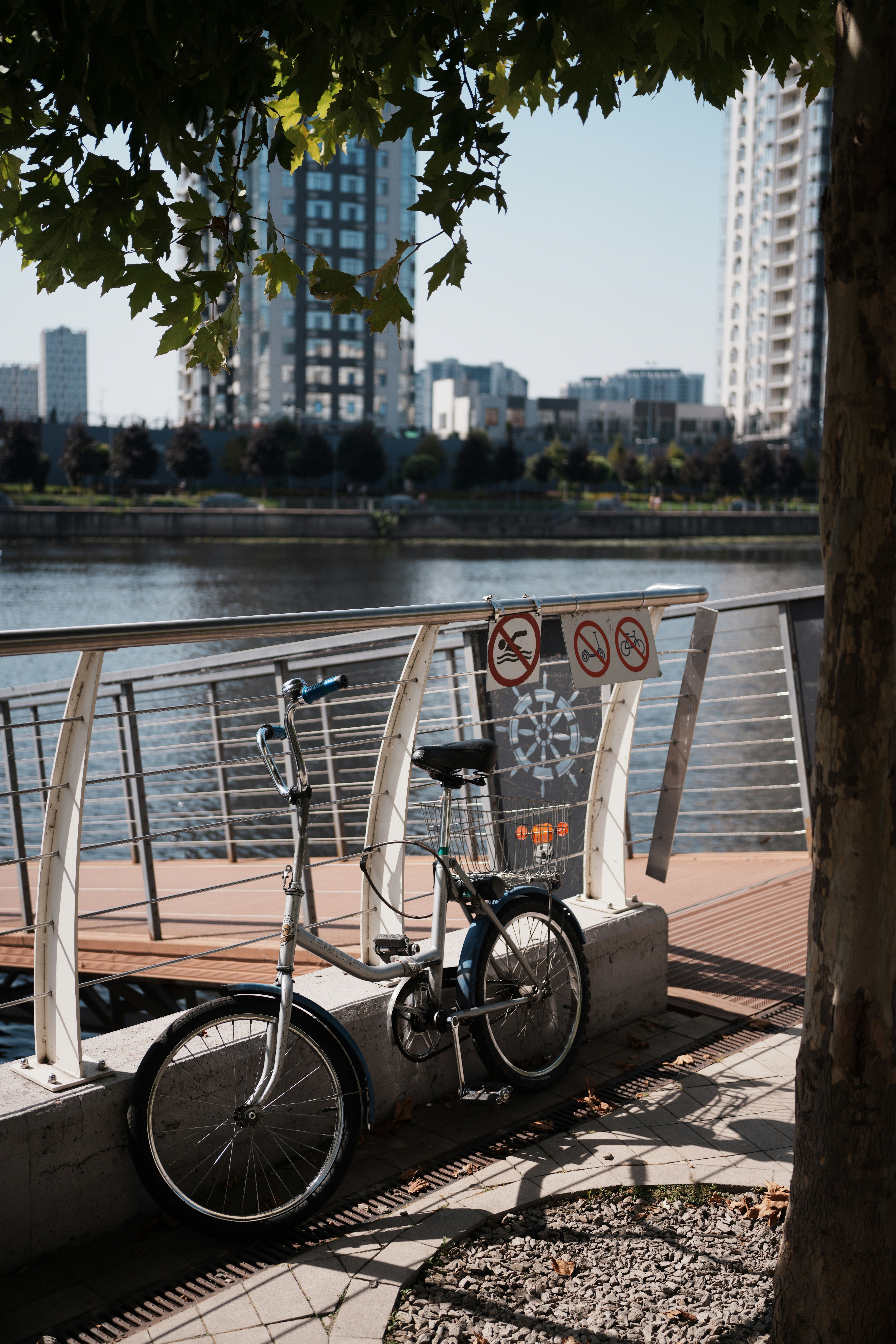 A bicycle parked by a river with cityscape background.