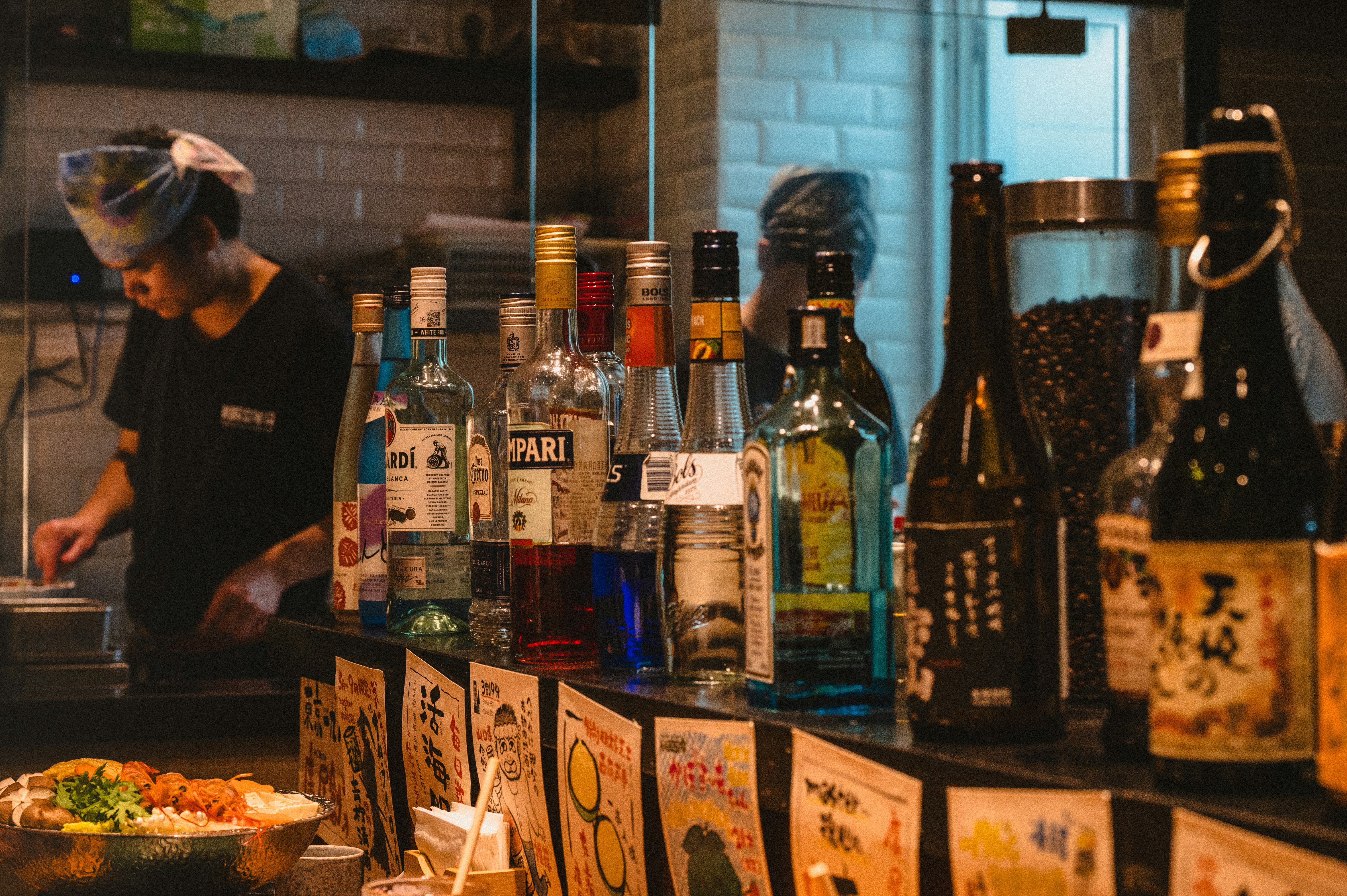 O.0 | Bartender preparing drinks behind a bar with bottles.