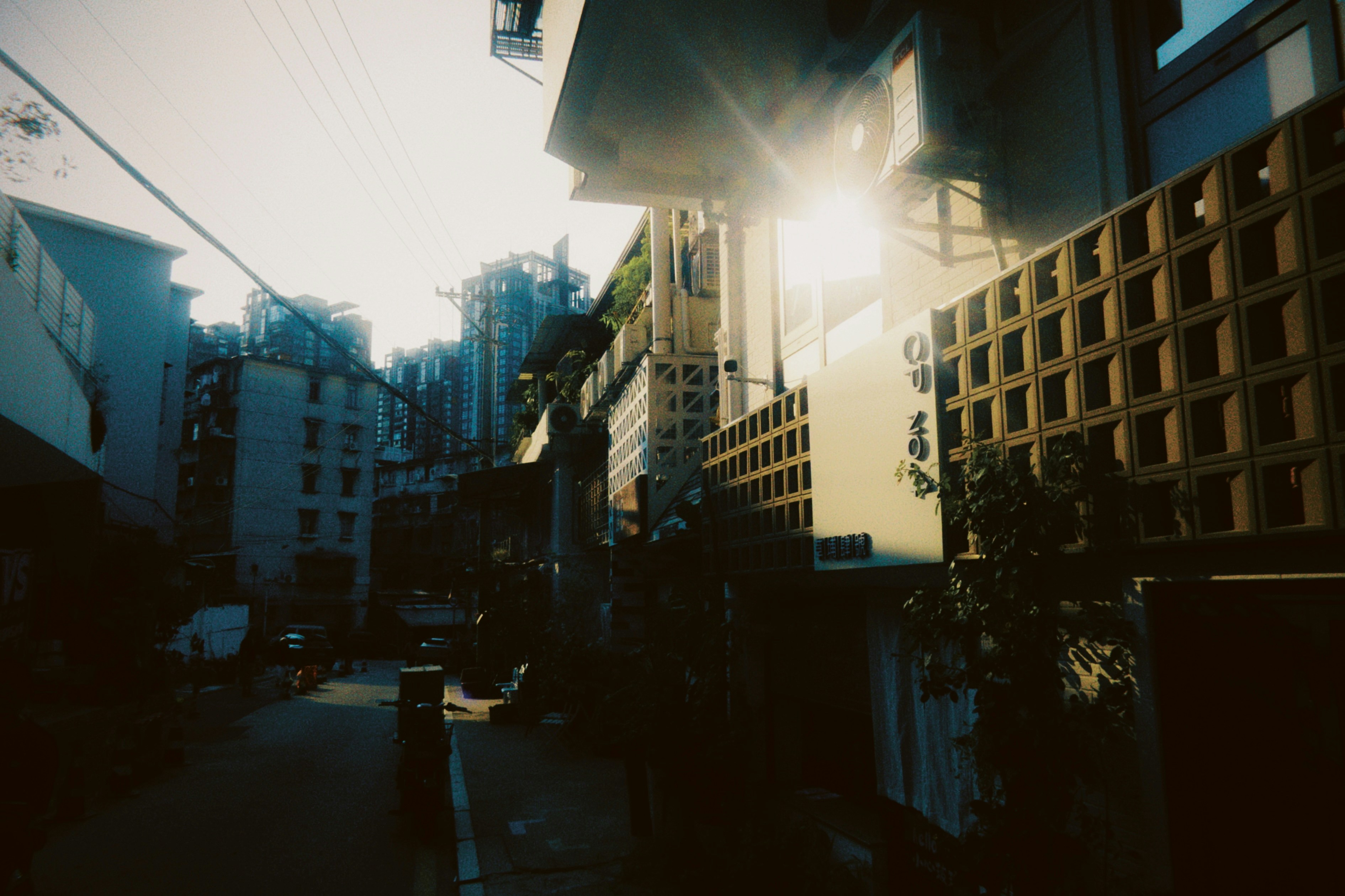 Sunlight filtering through buildings in a bustling urban alley, highlighting architectural details and everyday life.