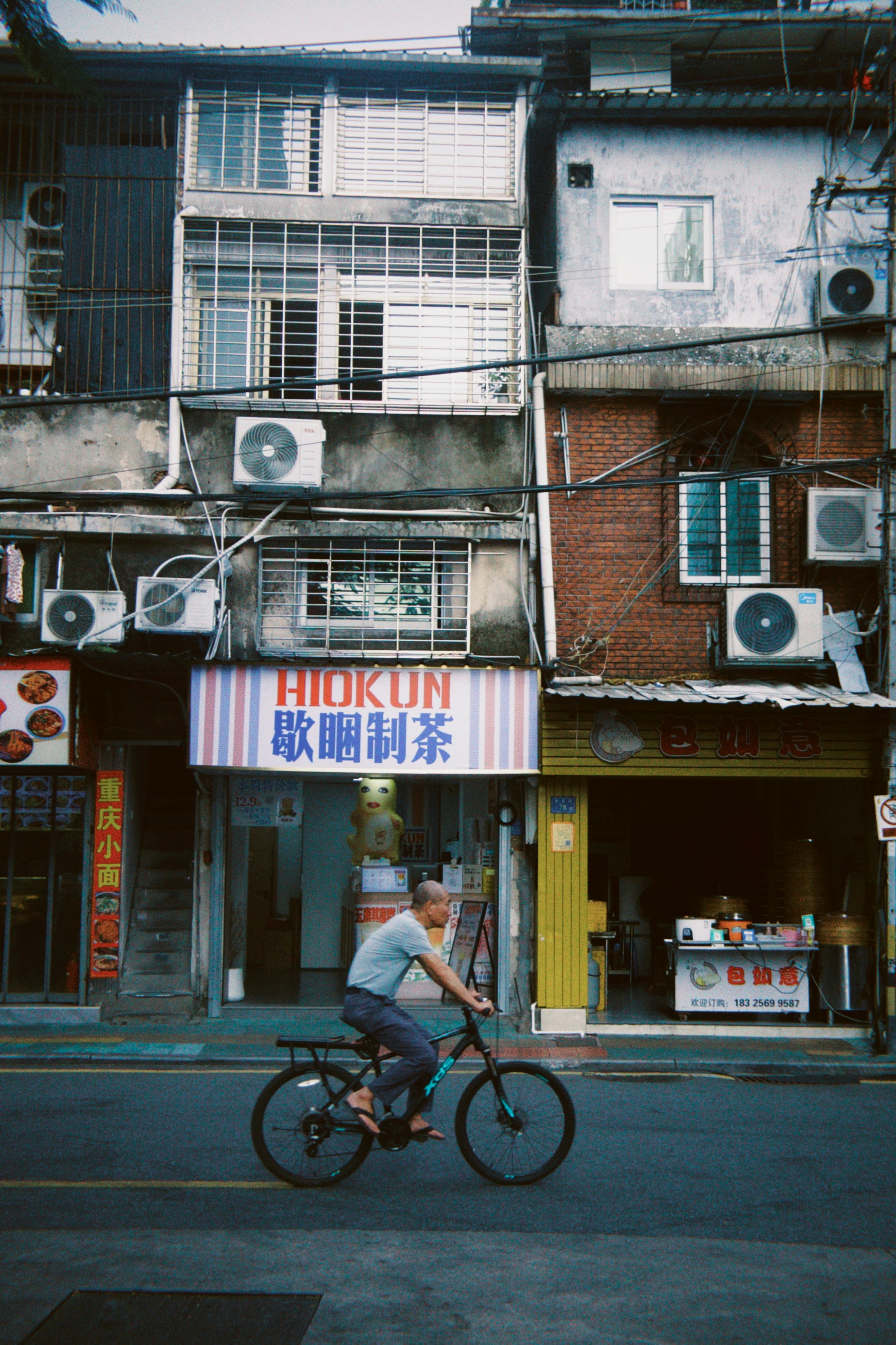 Man rides bicycle past storefronts with air conditioners. photo – Free ...