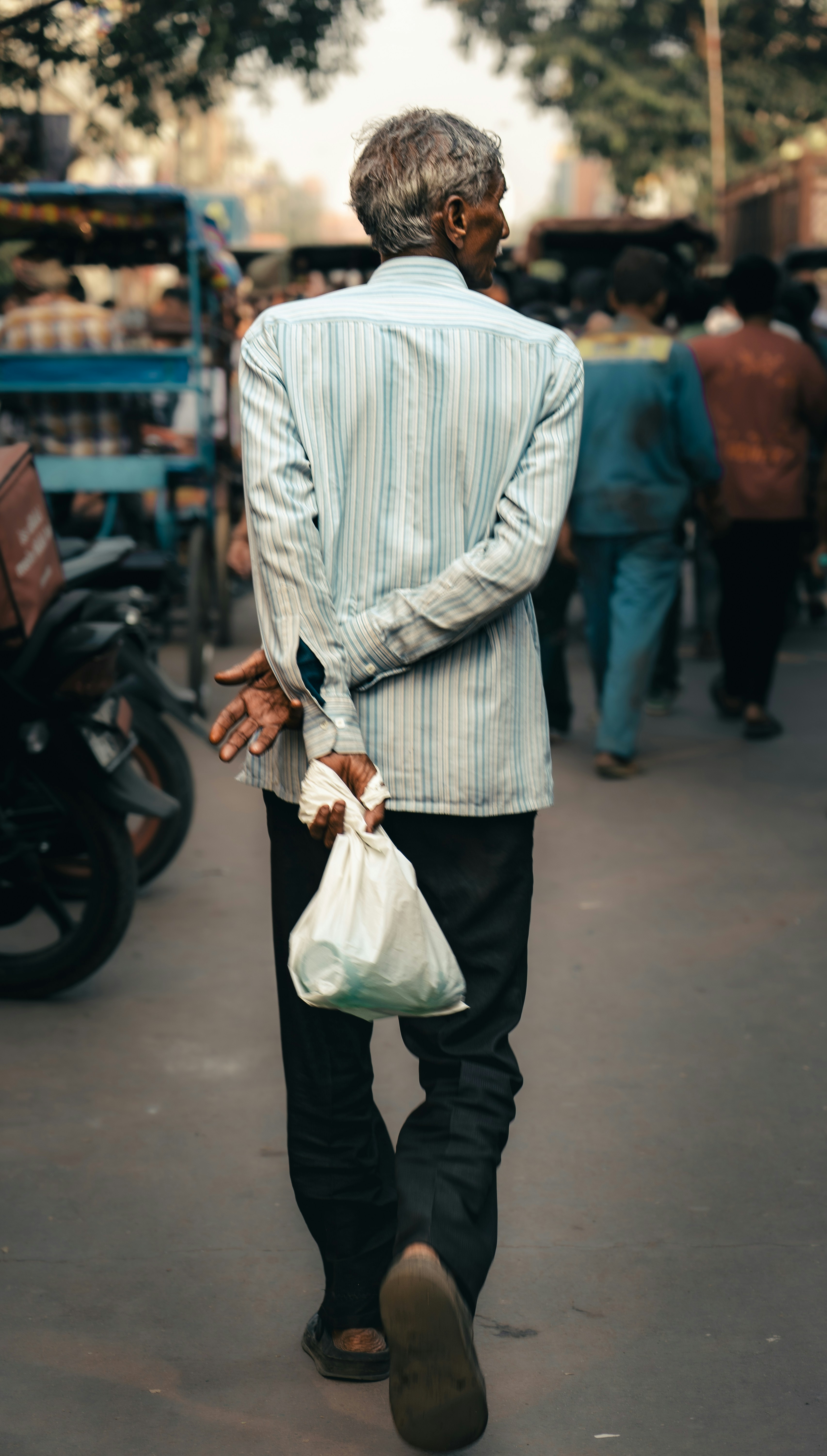 Elderly man walking with bag in busy street.