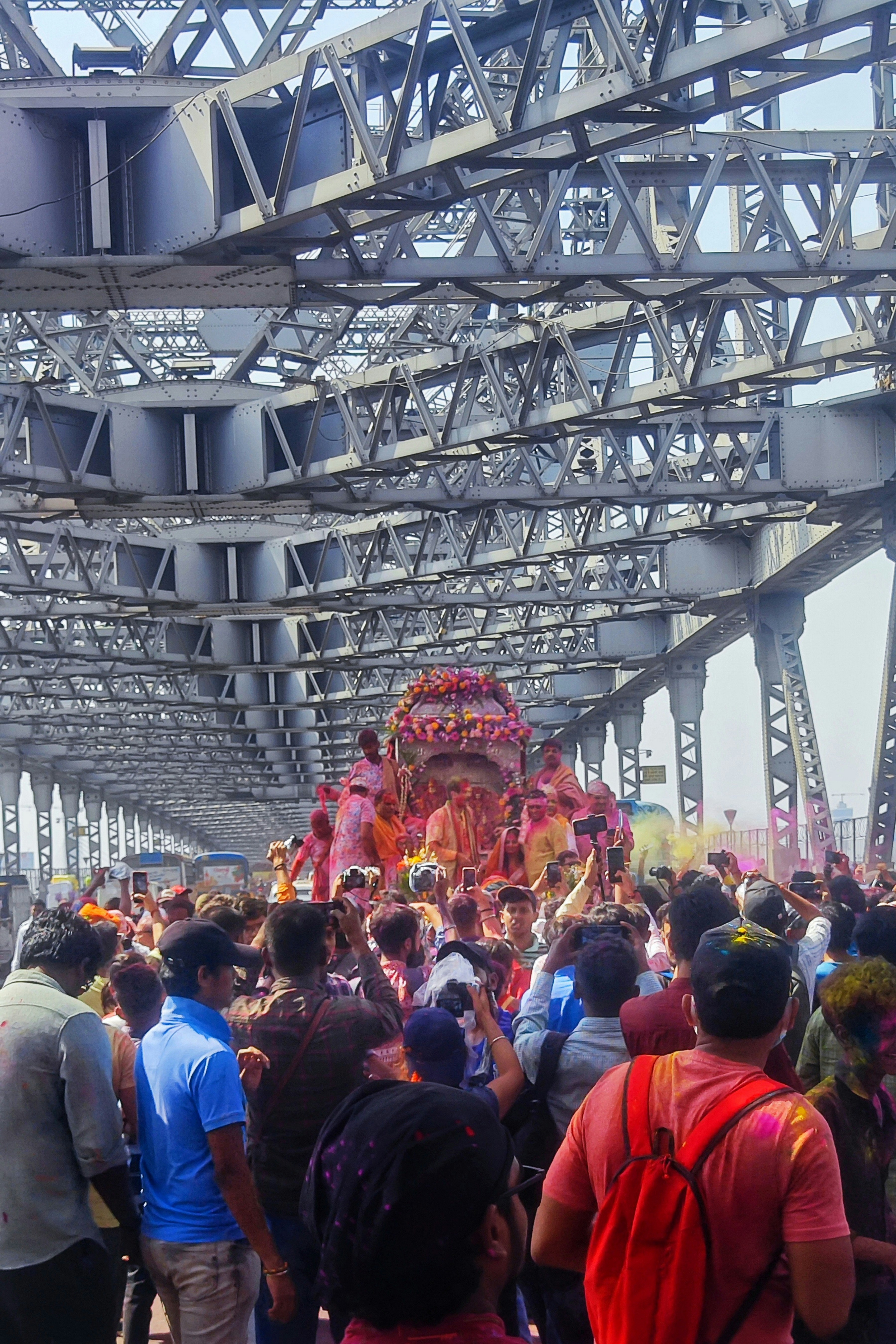 People celebrating holi on a bridge with a decorated float.