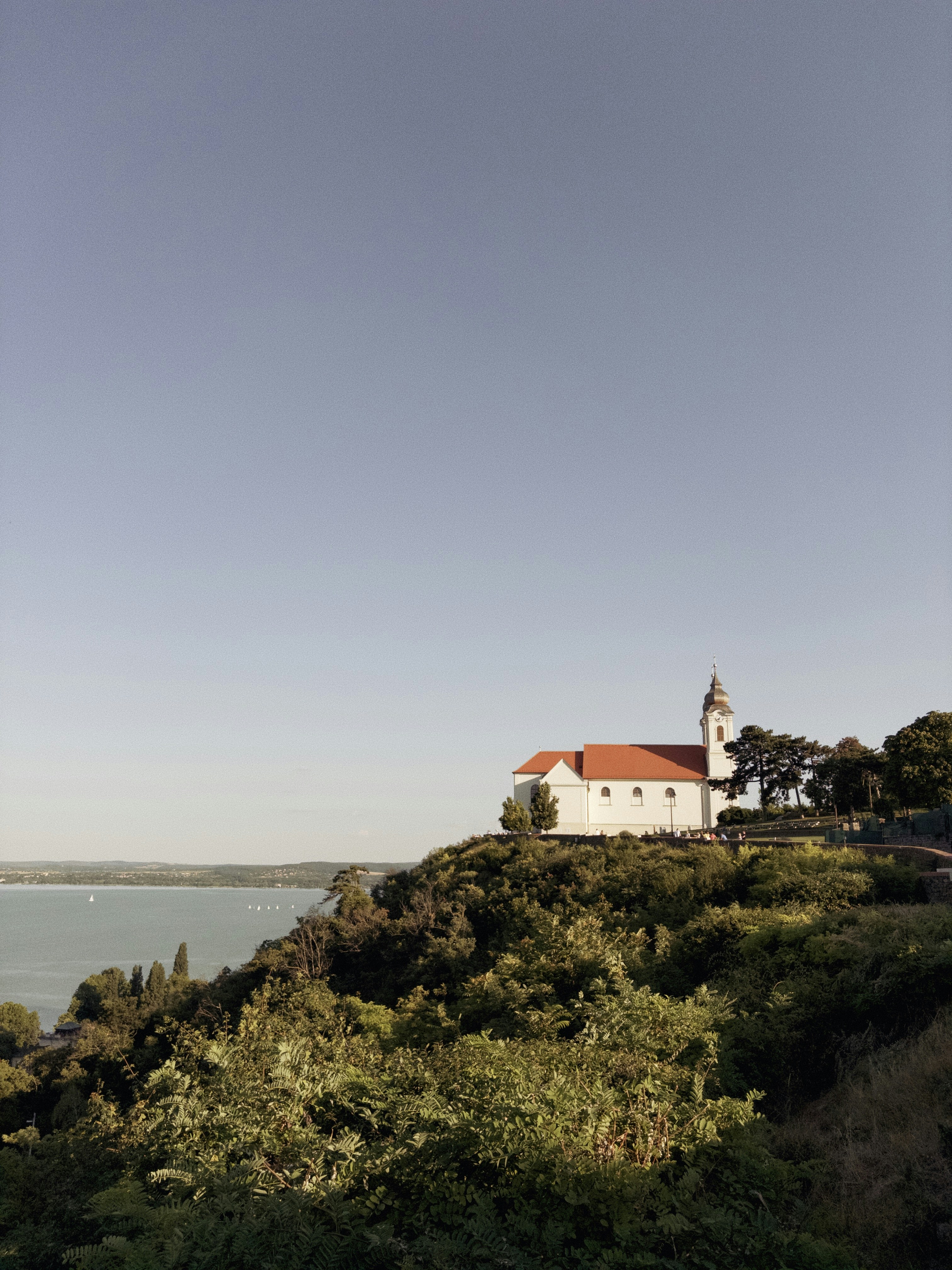 Tihanyi apátság | White church with red roof on a hill overlooking a body of water.