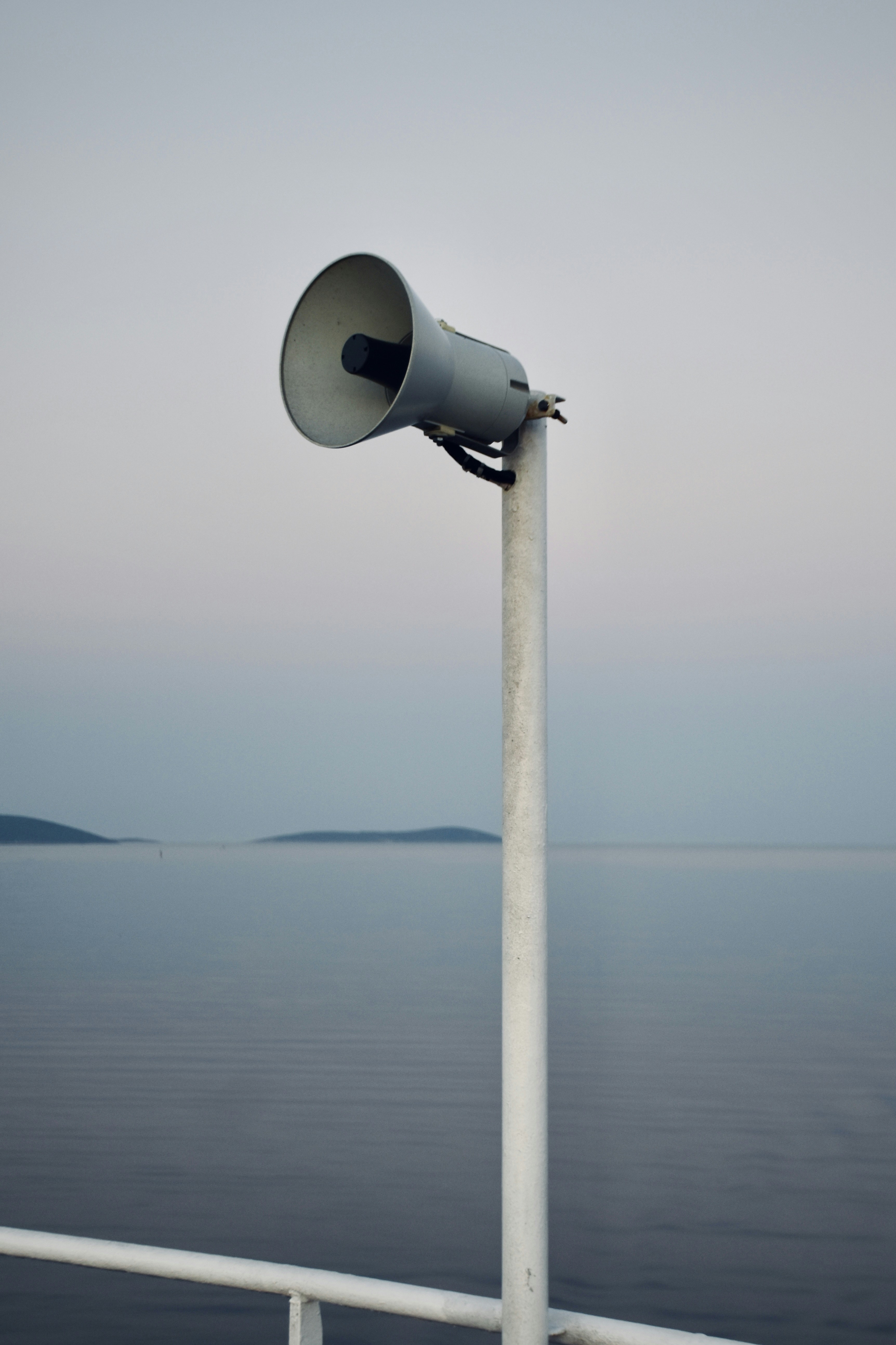 A speaker on a ship at dawn. | Loudspeaker mounted on pole over calm sea