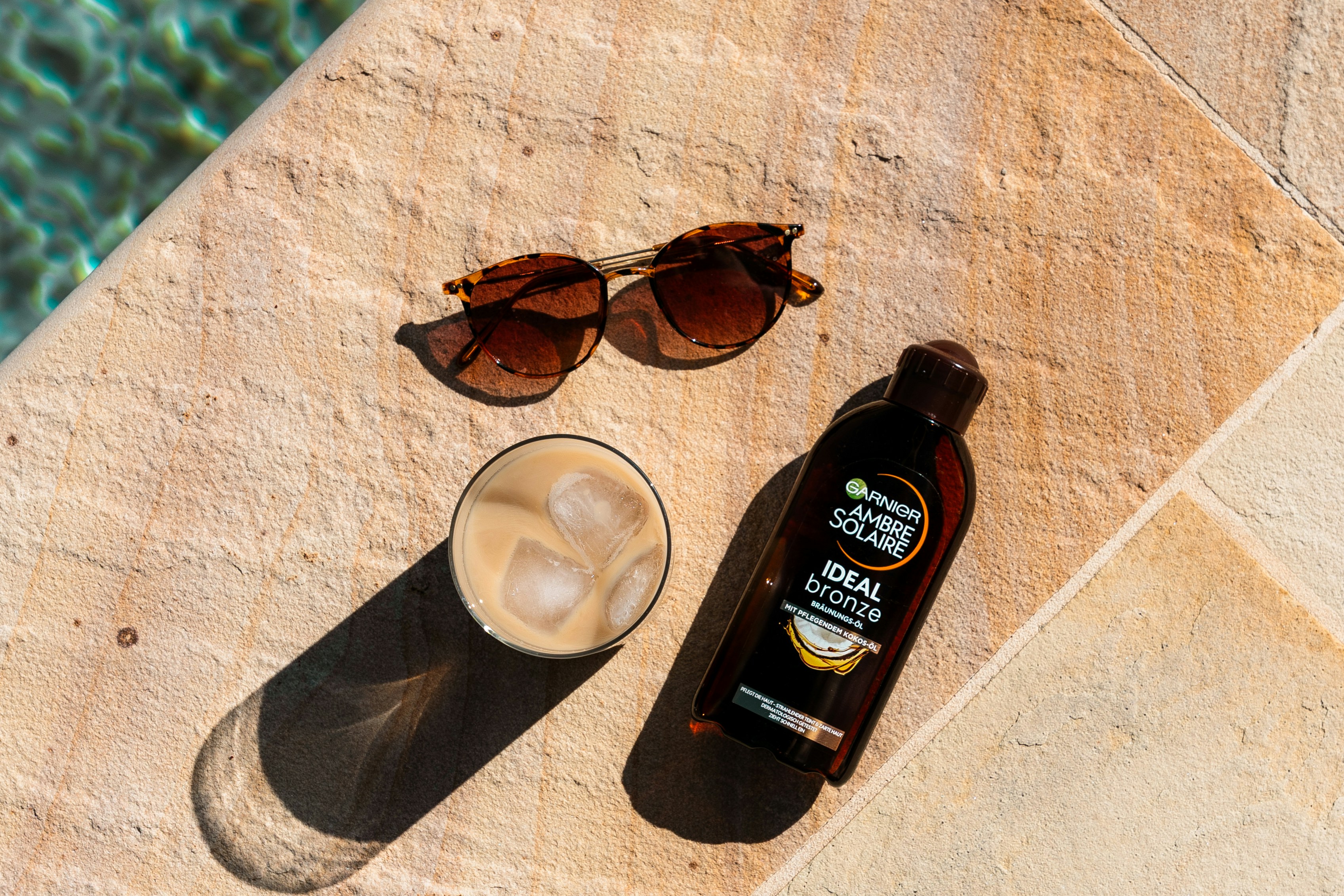 Sunglasses, drink, and tanning oil by pool