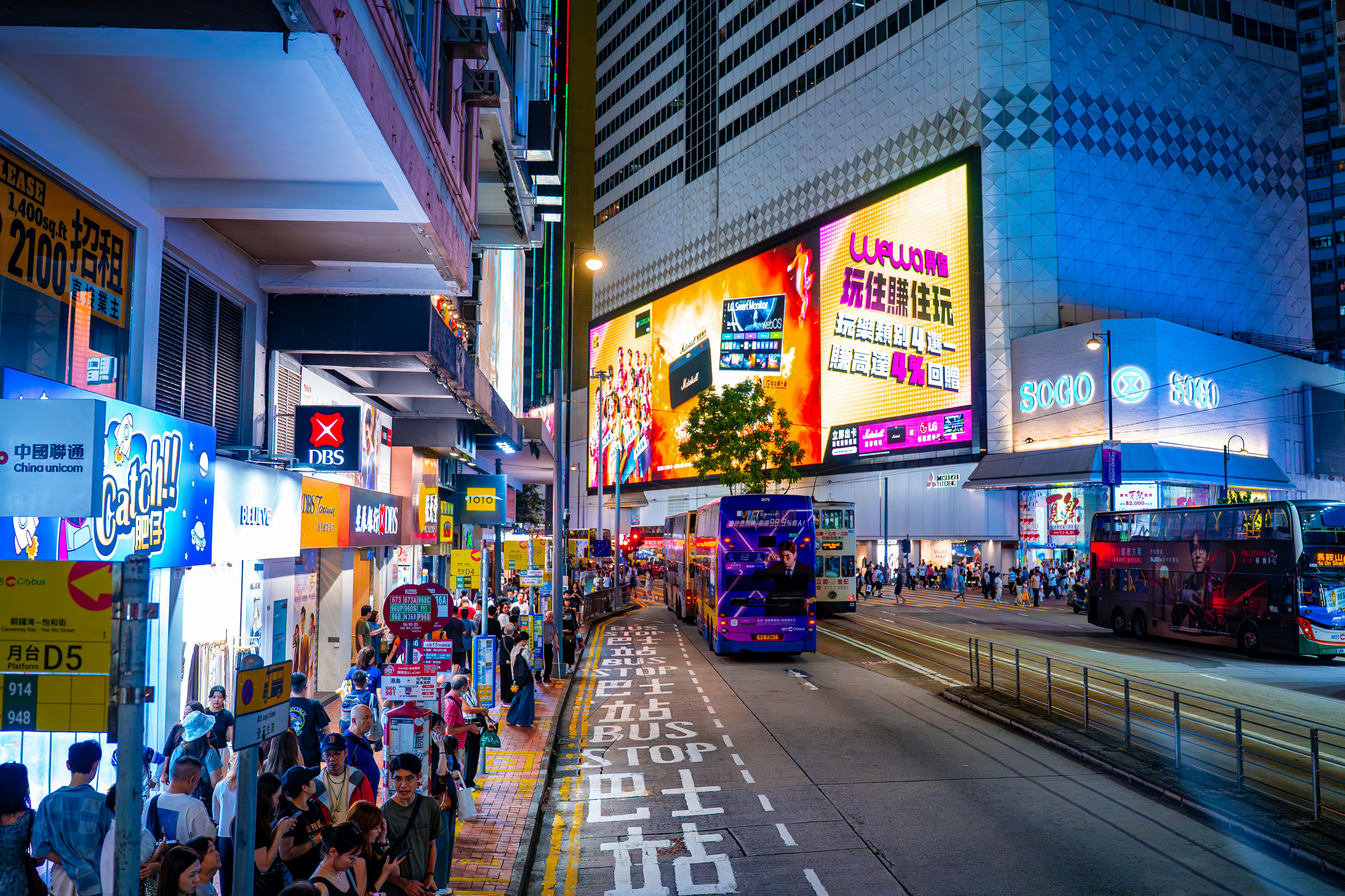 Bustling city street with neon signs and buses at night.