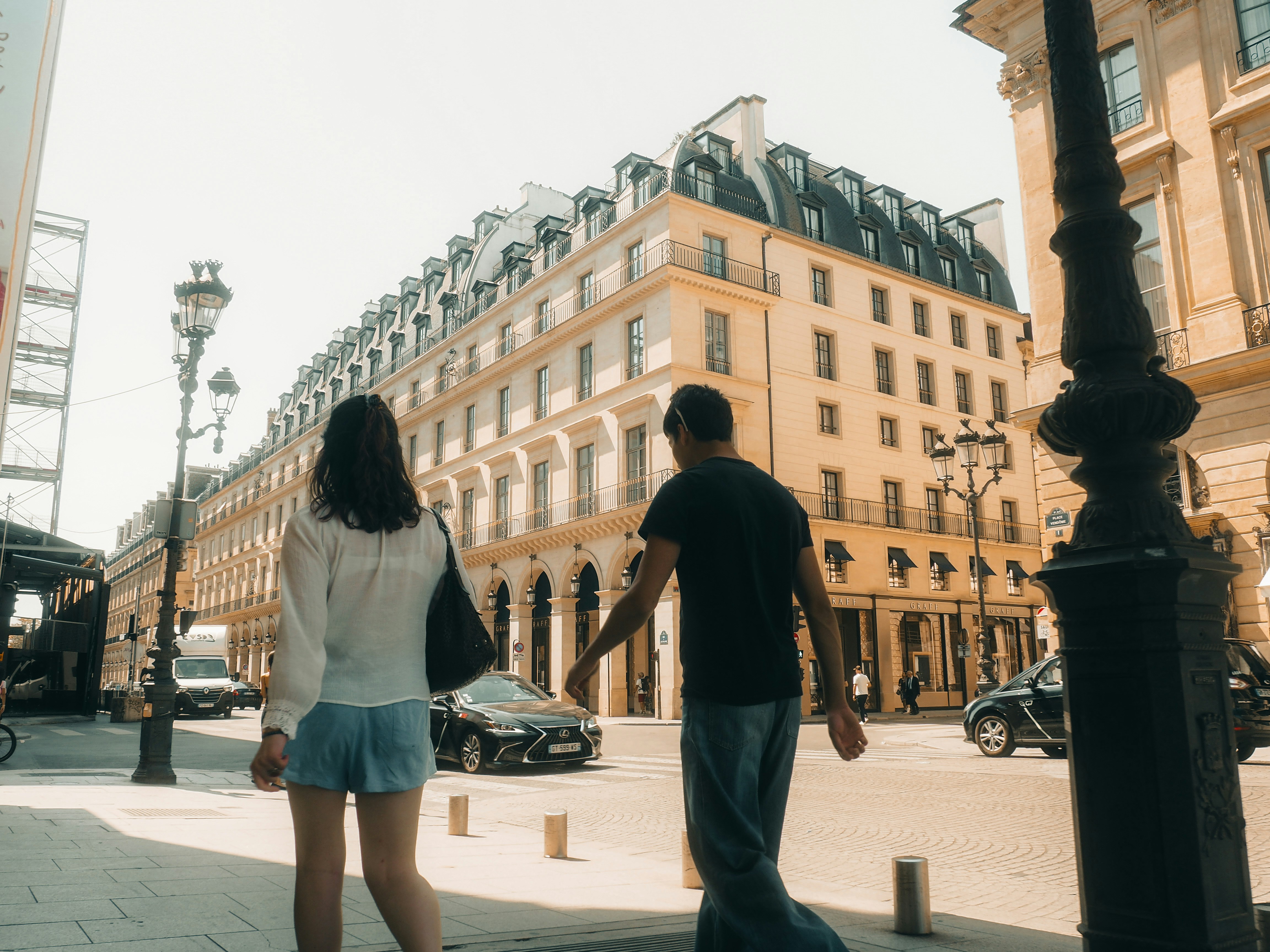 This image is a postcard of Paris city life: golden facades, endless rows of windows, elegant French architecture, and the lively urban rhythm of people walking. The photo mixes classic building design with modern cars and street details, showing how the city blends history and modernity. Perfect symmetry, perspective lines, and the contrast of light and shadow make it strong for architectural photography. The shot captures daily moments, travel vibes, and the unmistakable Paris mood. It is both historic and modern, both cinematic and authentic, exactly what people search for when dreaming of | Couple walking on a sunny street in paris.