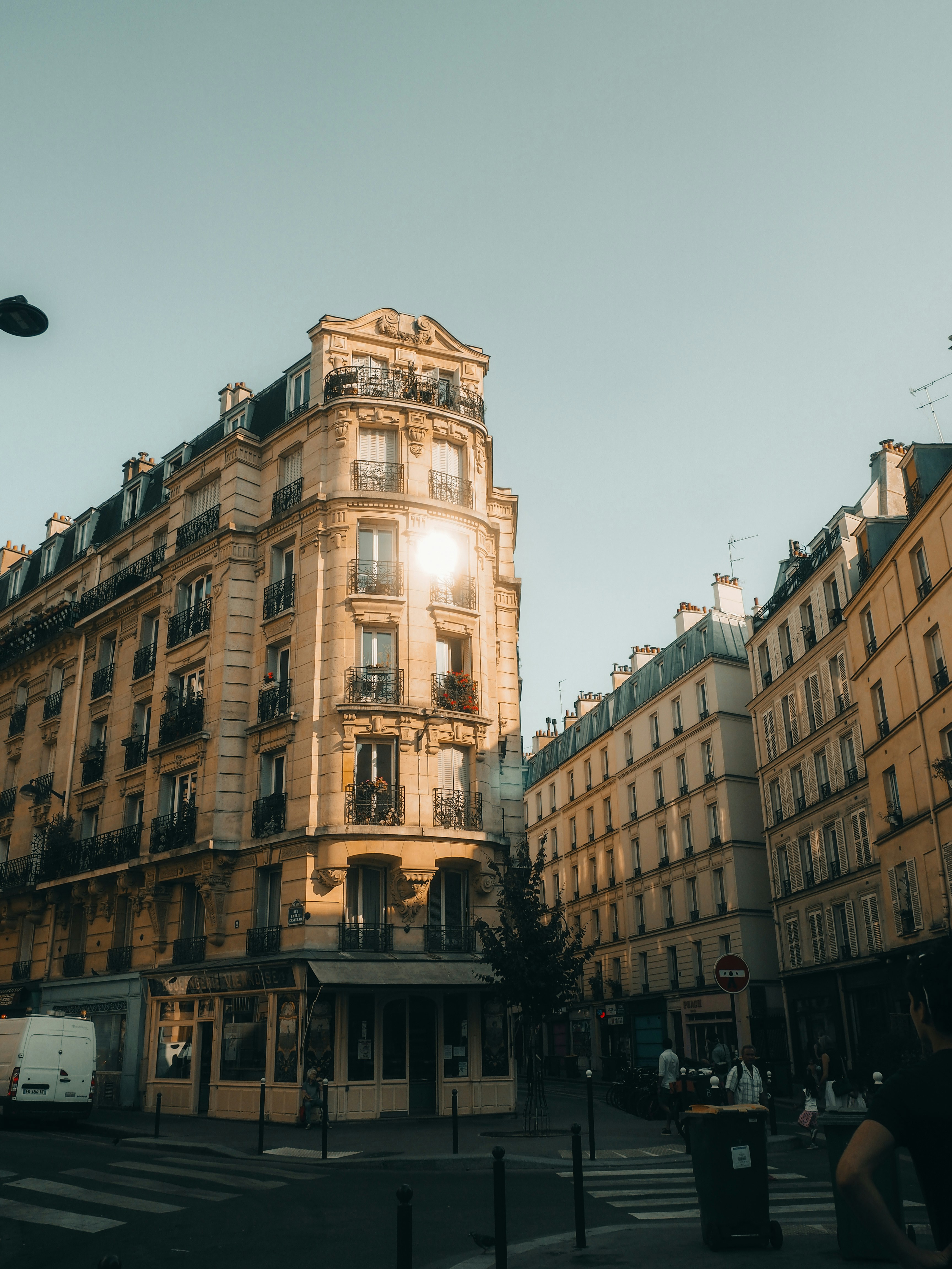 A sunlit Parisian building reflects warm light, showcasing intricate architecture amidst bustling streets.