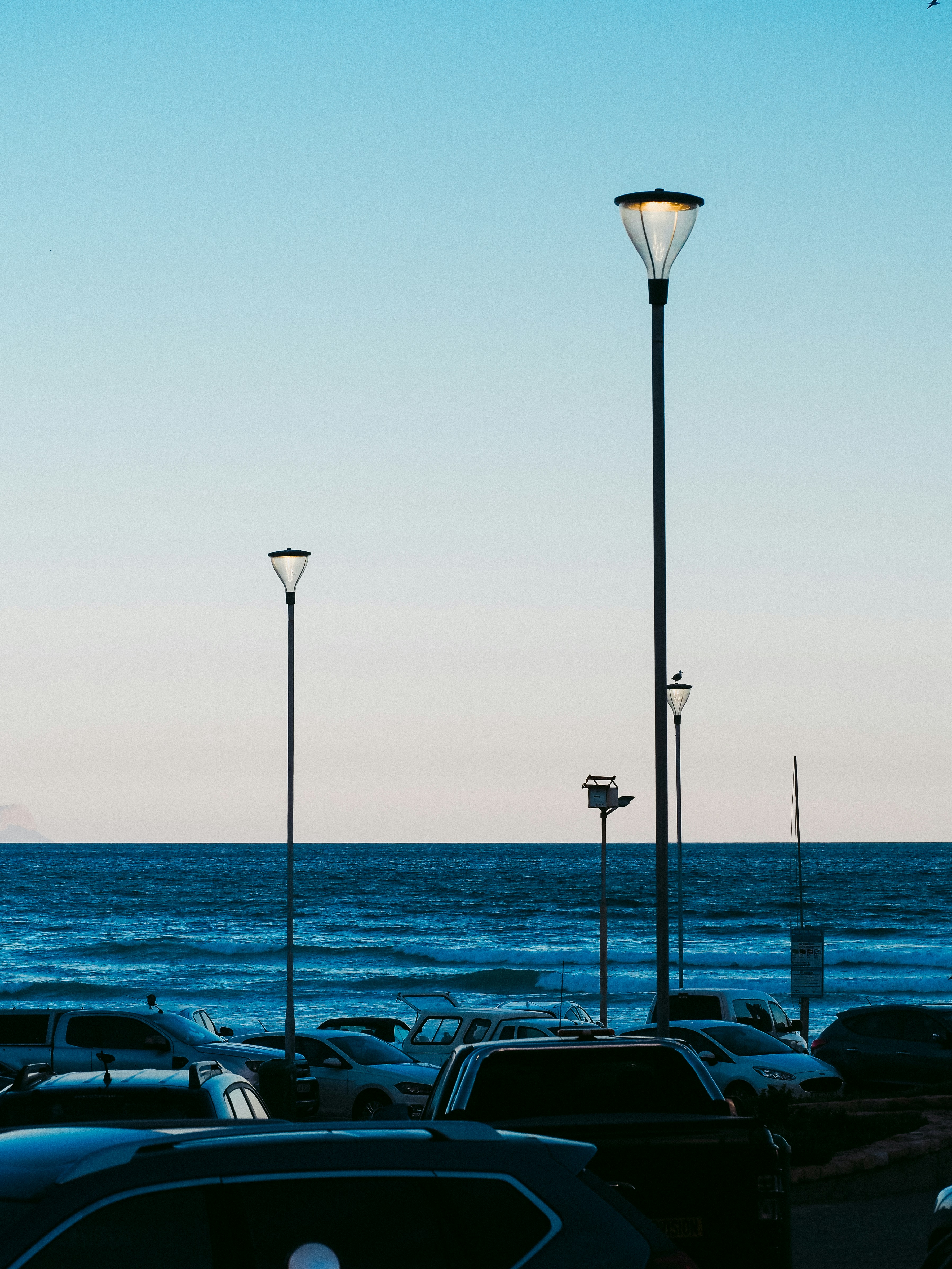 Cape Town evenings by the sea feel effortlessly magical — the streetlights glow softly as the ocean breeze drifts through, cars gathered after a day of adventure, and the horizon promises another story tomorrow. A simple reminder of why coastal city life feels so alive. | Streetlights by the ocean at dusk