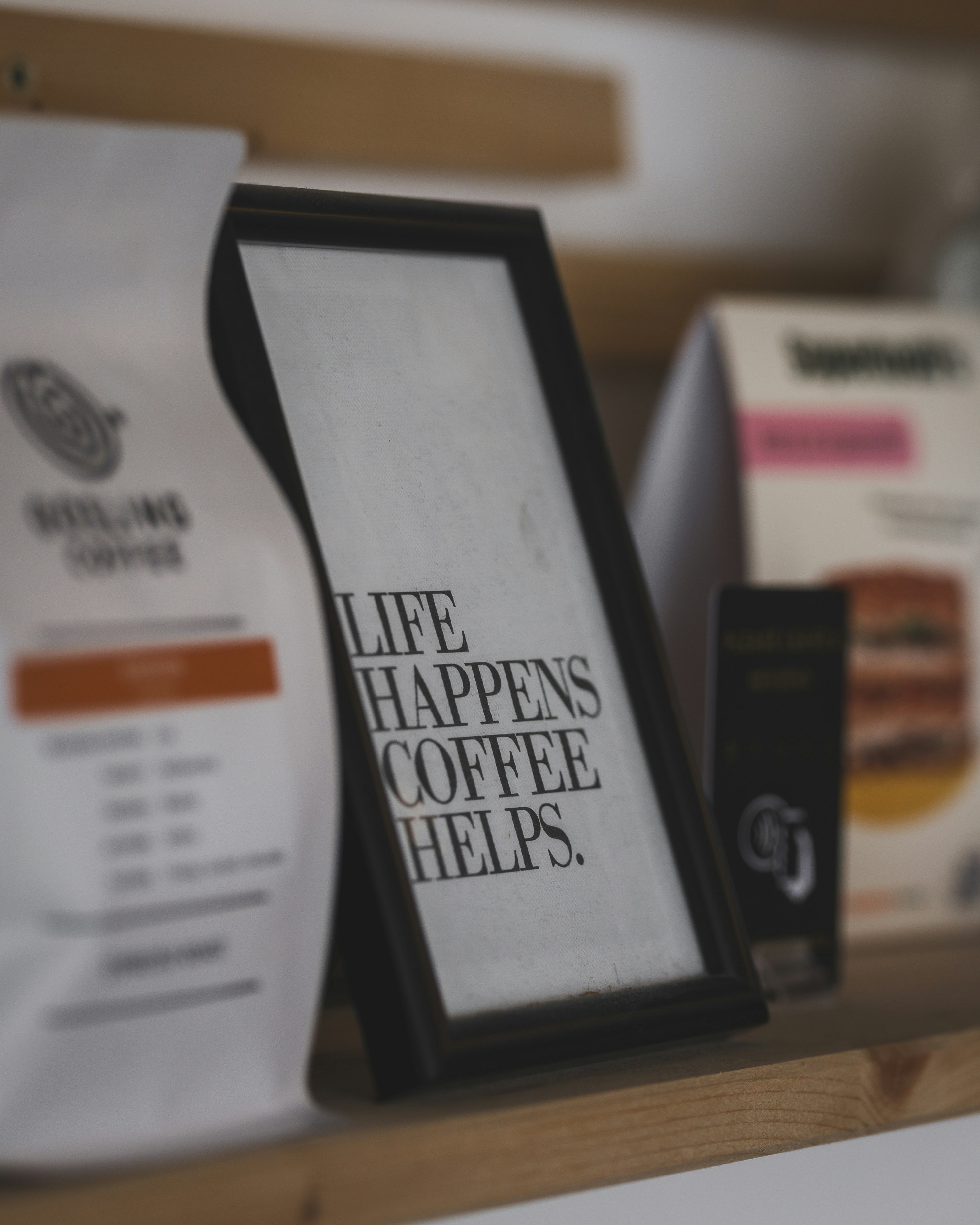 Framed quote emphasizing the importance of coffee, surrounded by coffee-related products on a shelf.