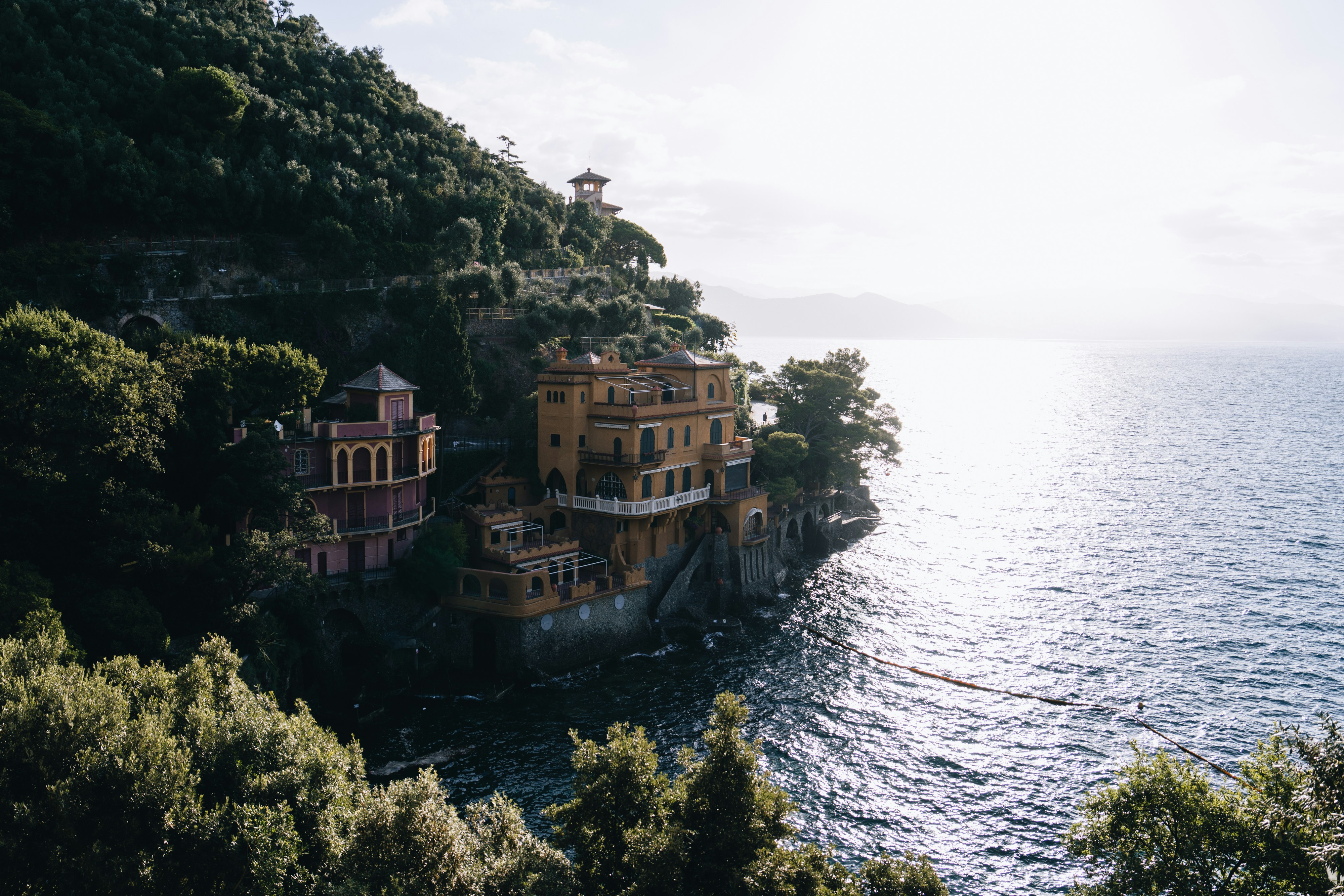 Colorful coastal villas nestled on a rocky shoreline, overlooking the shimmering sea under a soft, cloudy sky.