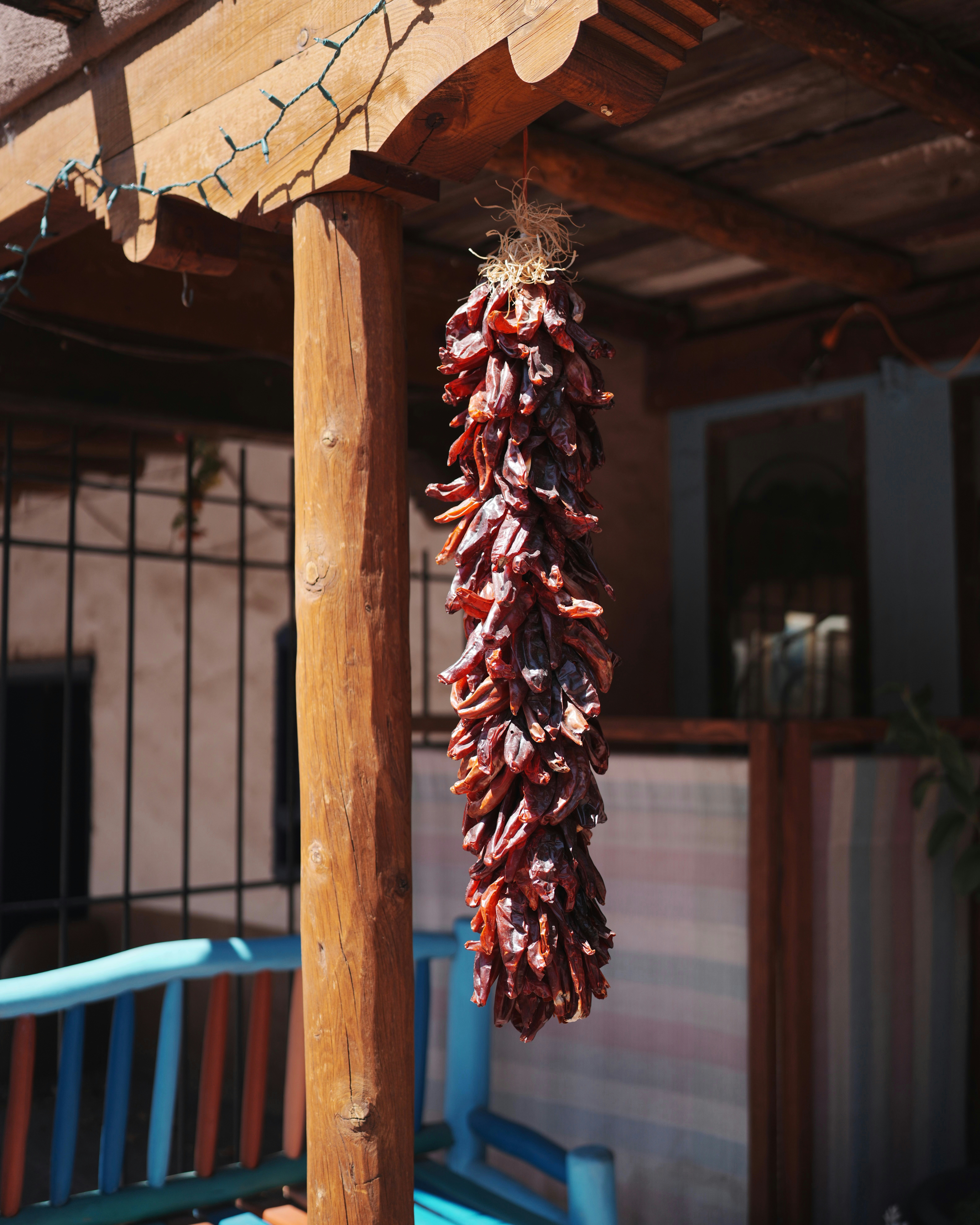 Dried red chili peppers hanging outdoors under a wooden structure.