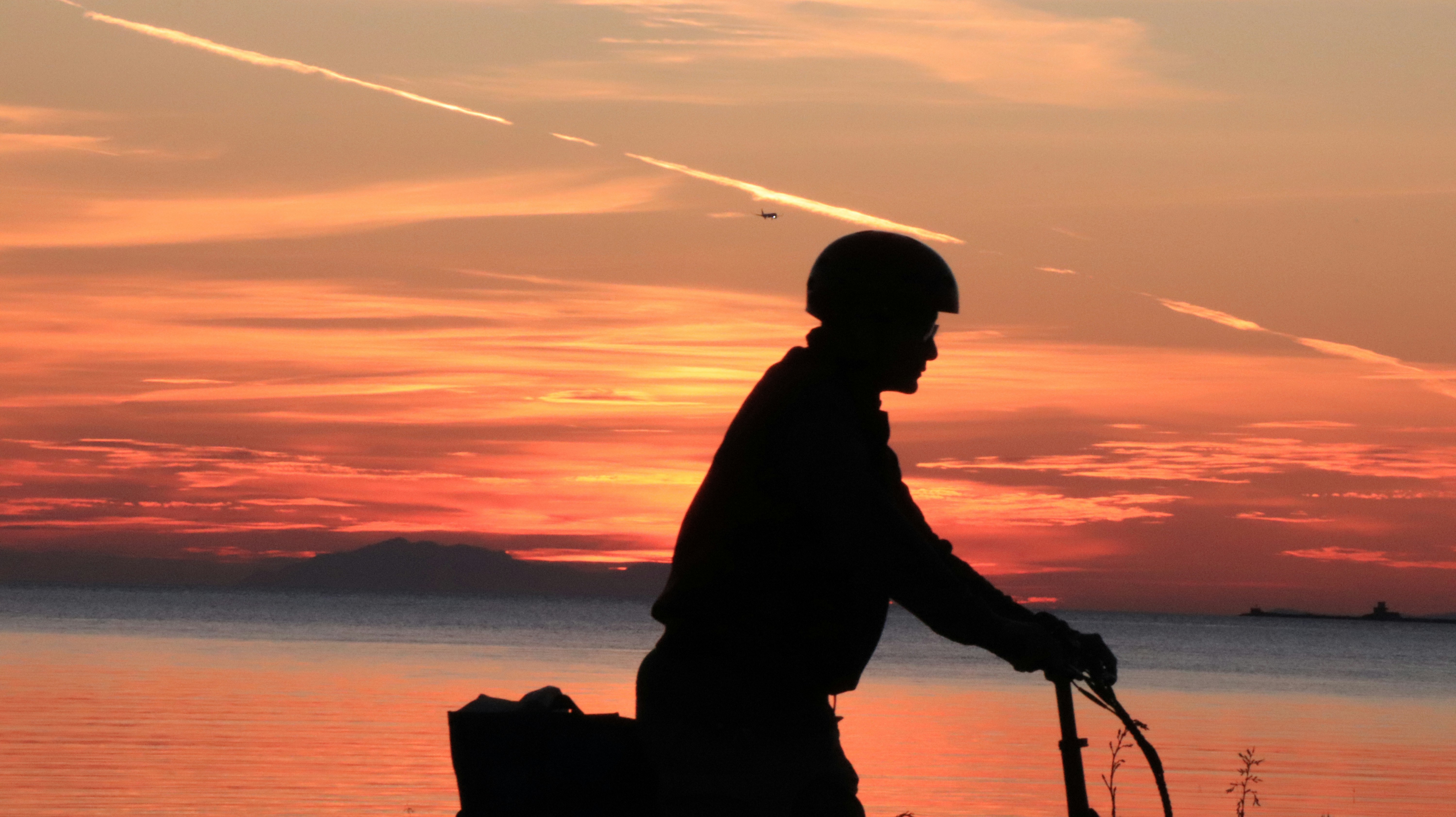 Silhouette of person riding scooter at sunset