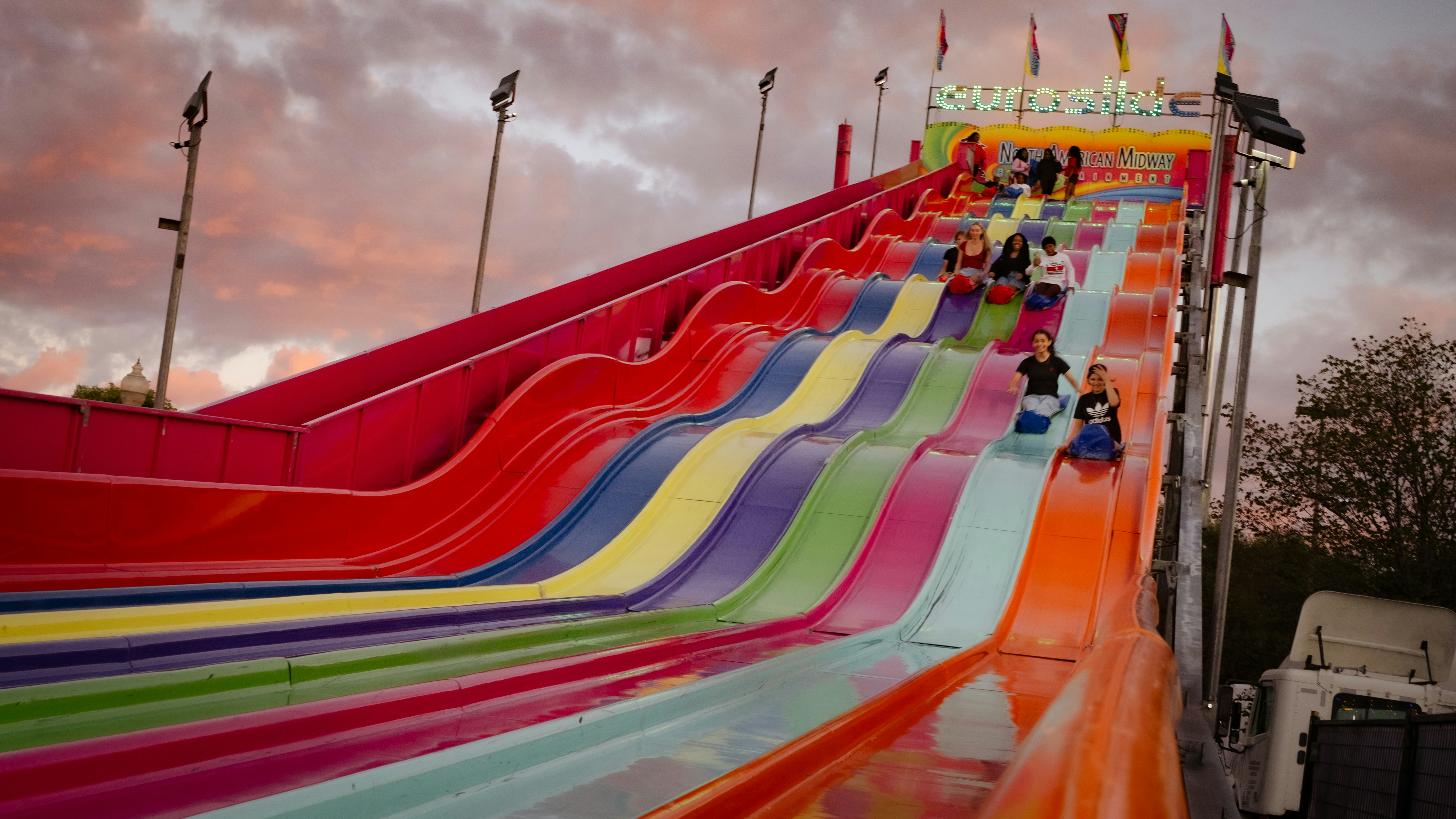 Summer time on the midway | People riding a colorful giant slide at dusk