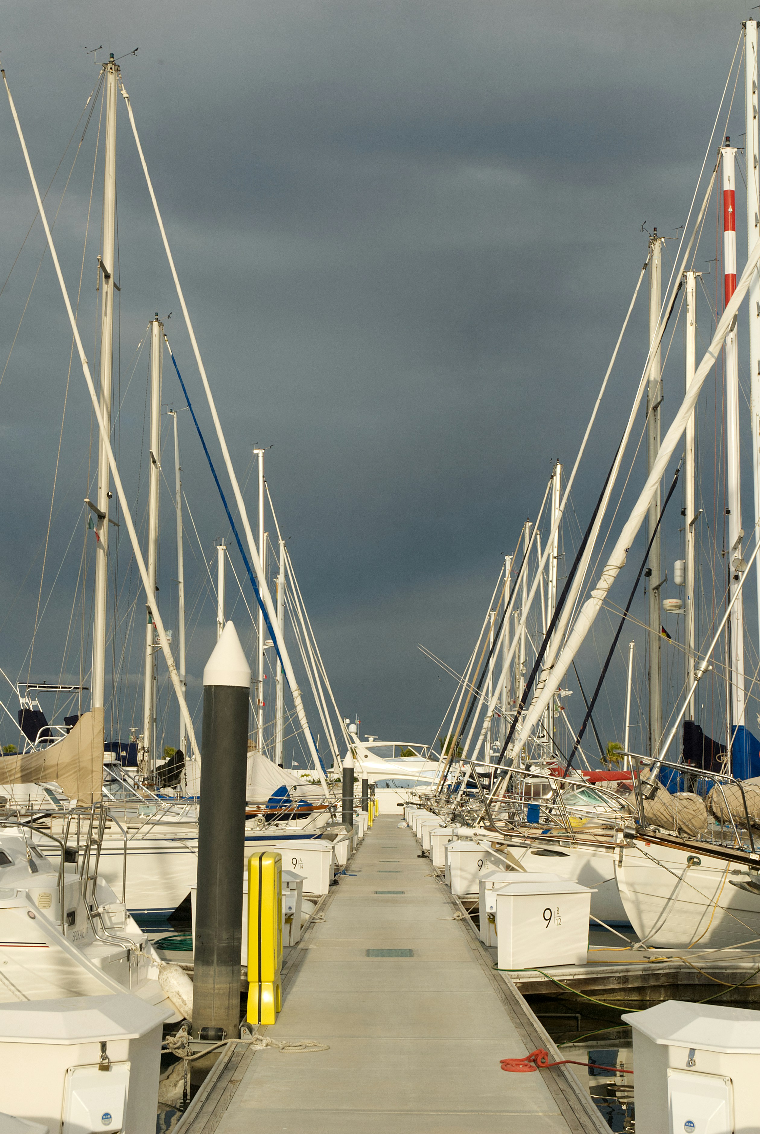 Many different boats at the docks | Sailboats docked at a marina under stormy skies.