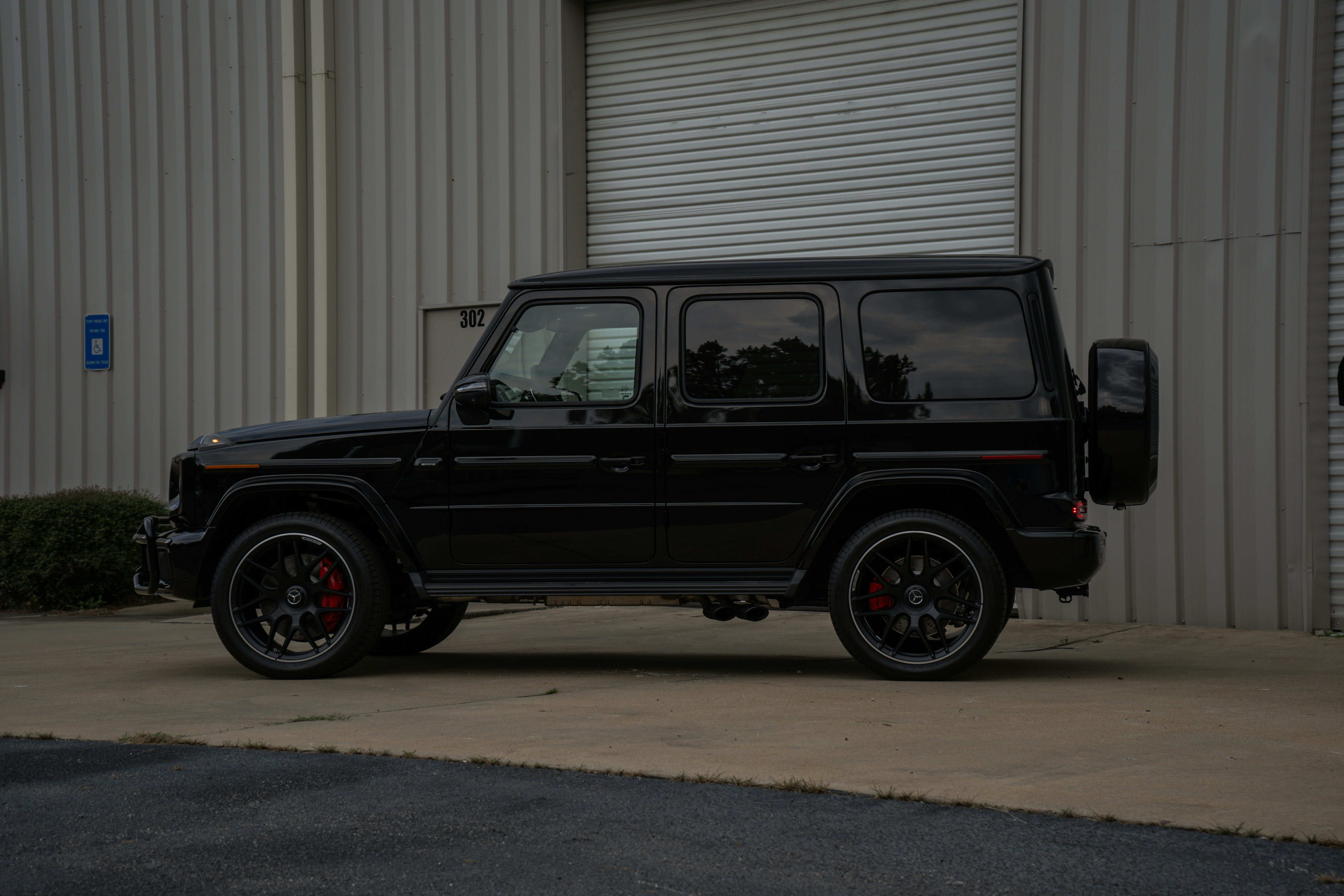 Black Mercedes-Benz G-Class parked in front of a metal building, showcasing its robust design and sleek lines.