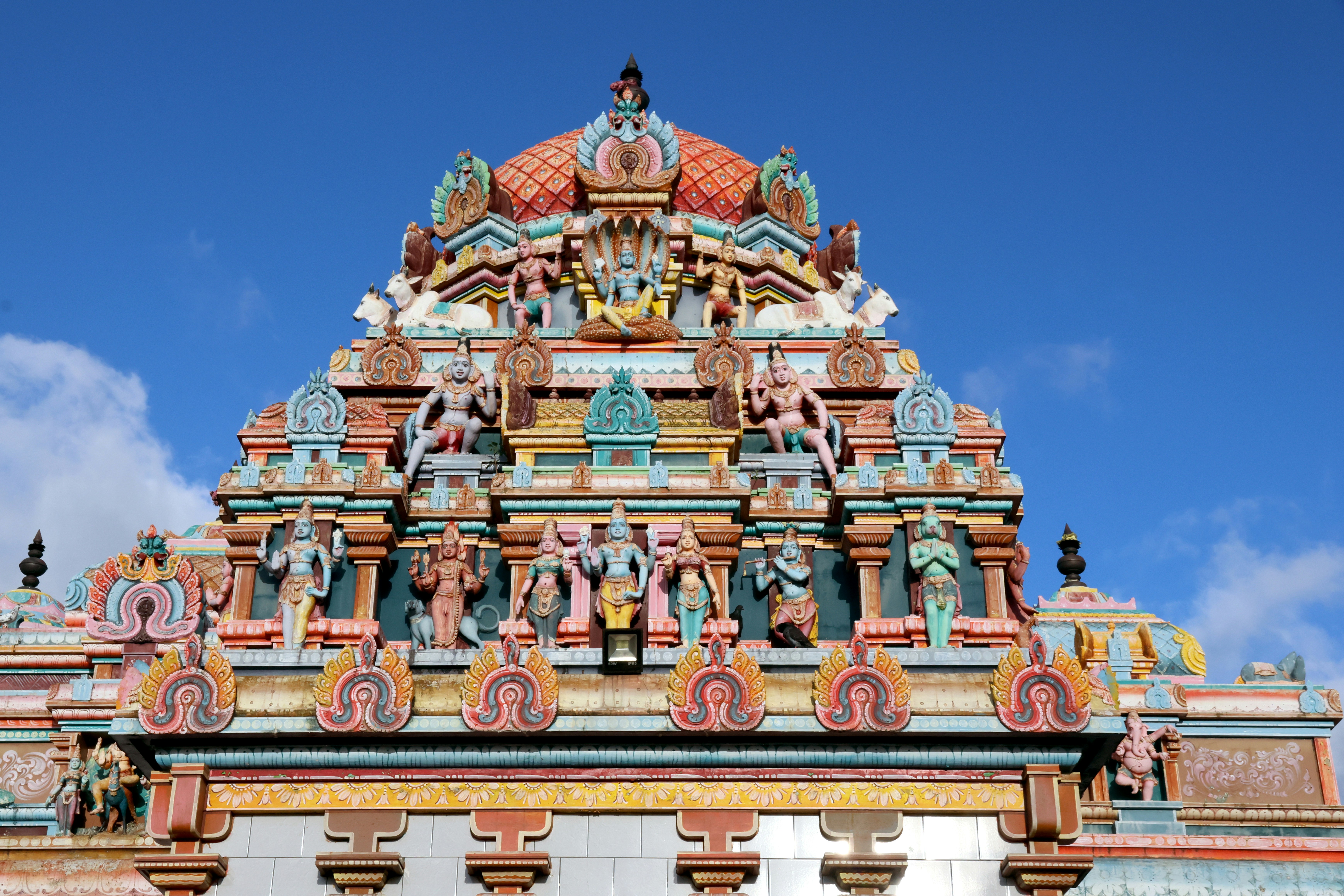 Intricately carved temple tower adorned with colorful sculptures and a striking dome against a clear blue sky.