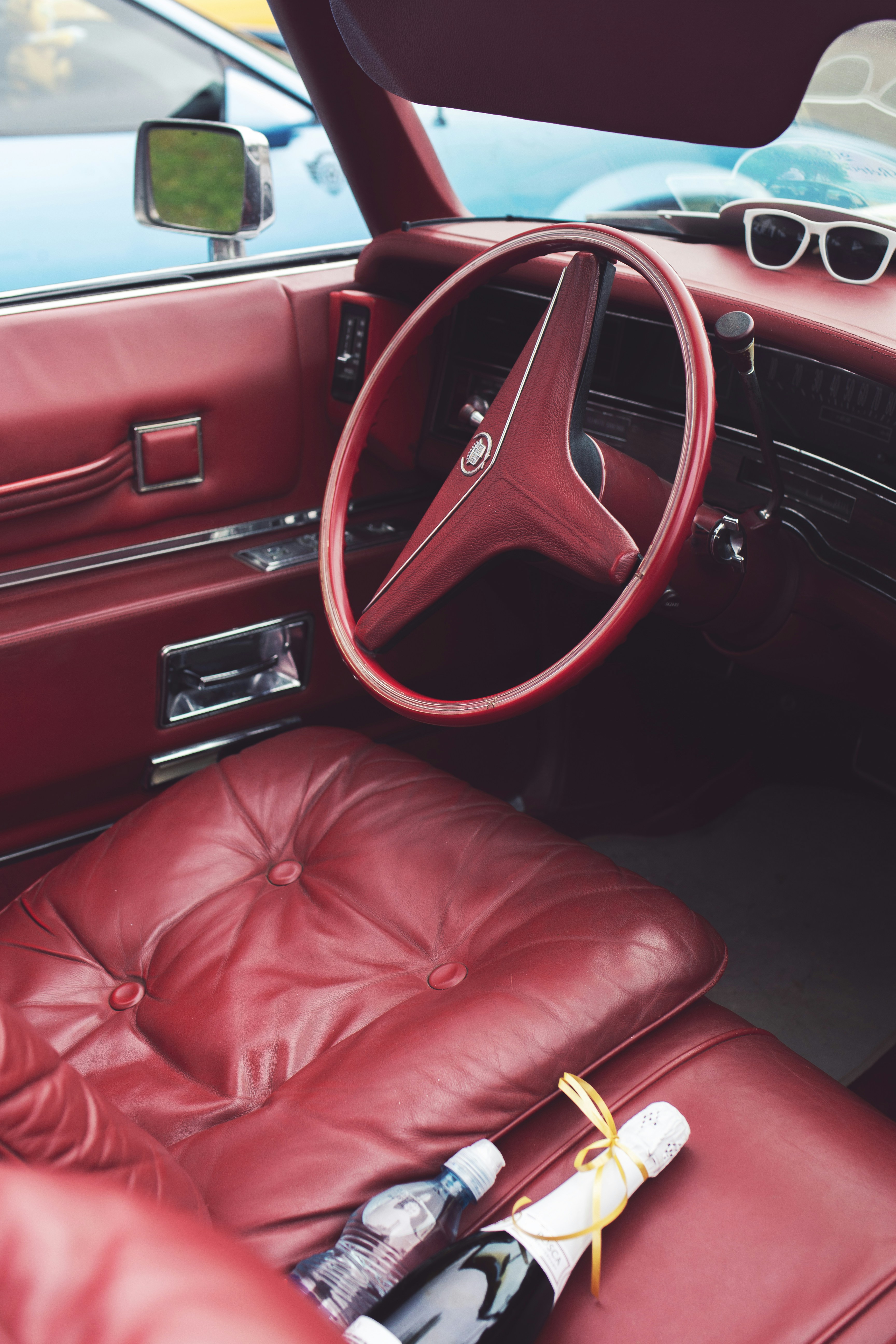 Interior of a classic car featuring rich red leather upholstery and a stylish steering wheel. Bottles of drinks are placed on the seat.