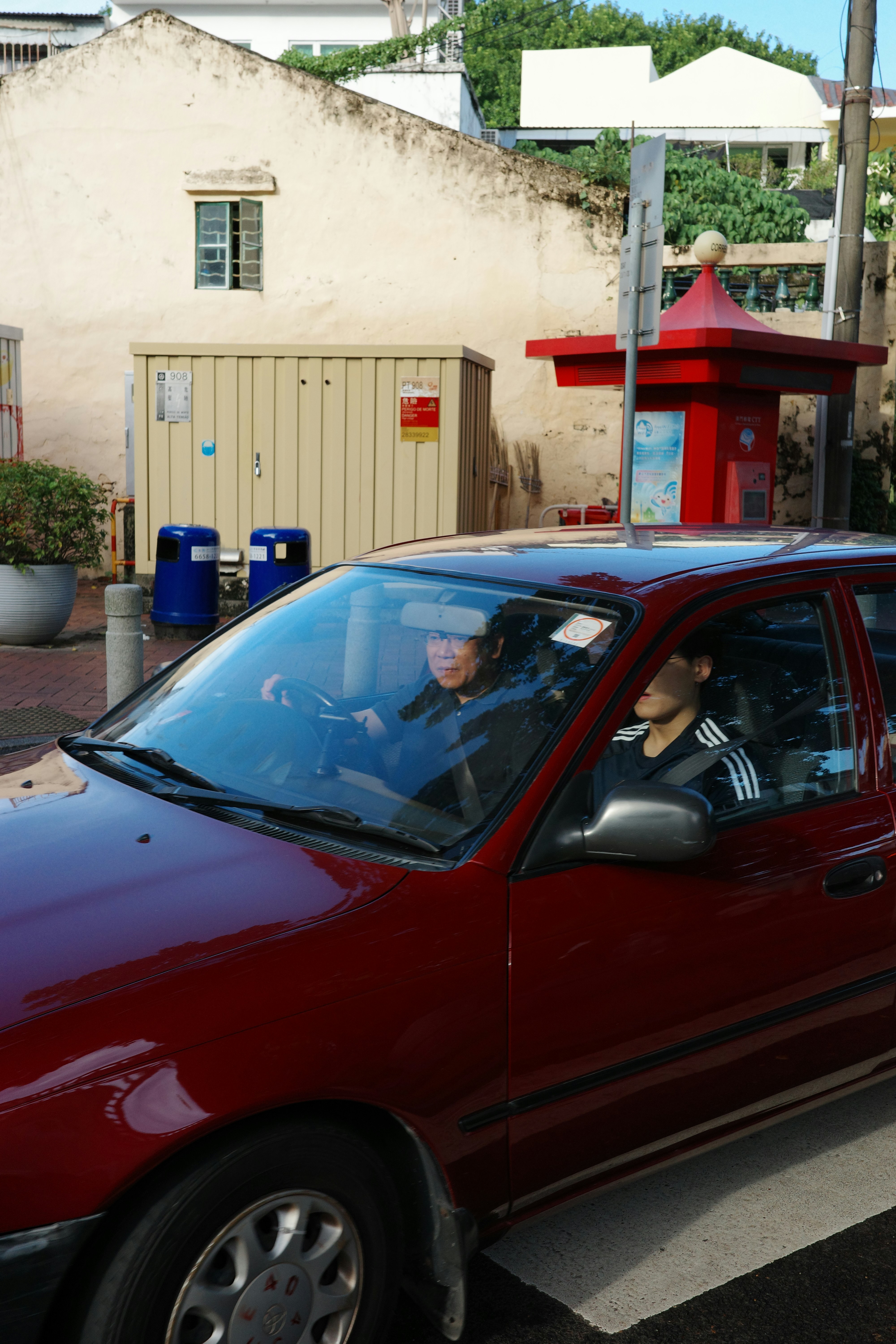 Red Sedan at a Sunlit Streetfront: Passengers in Transit