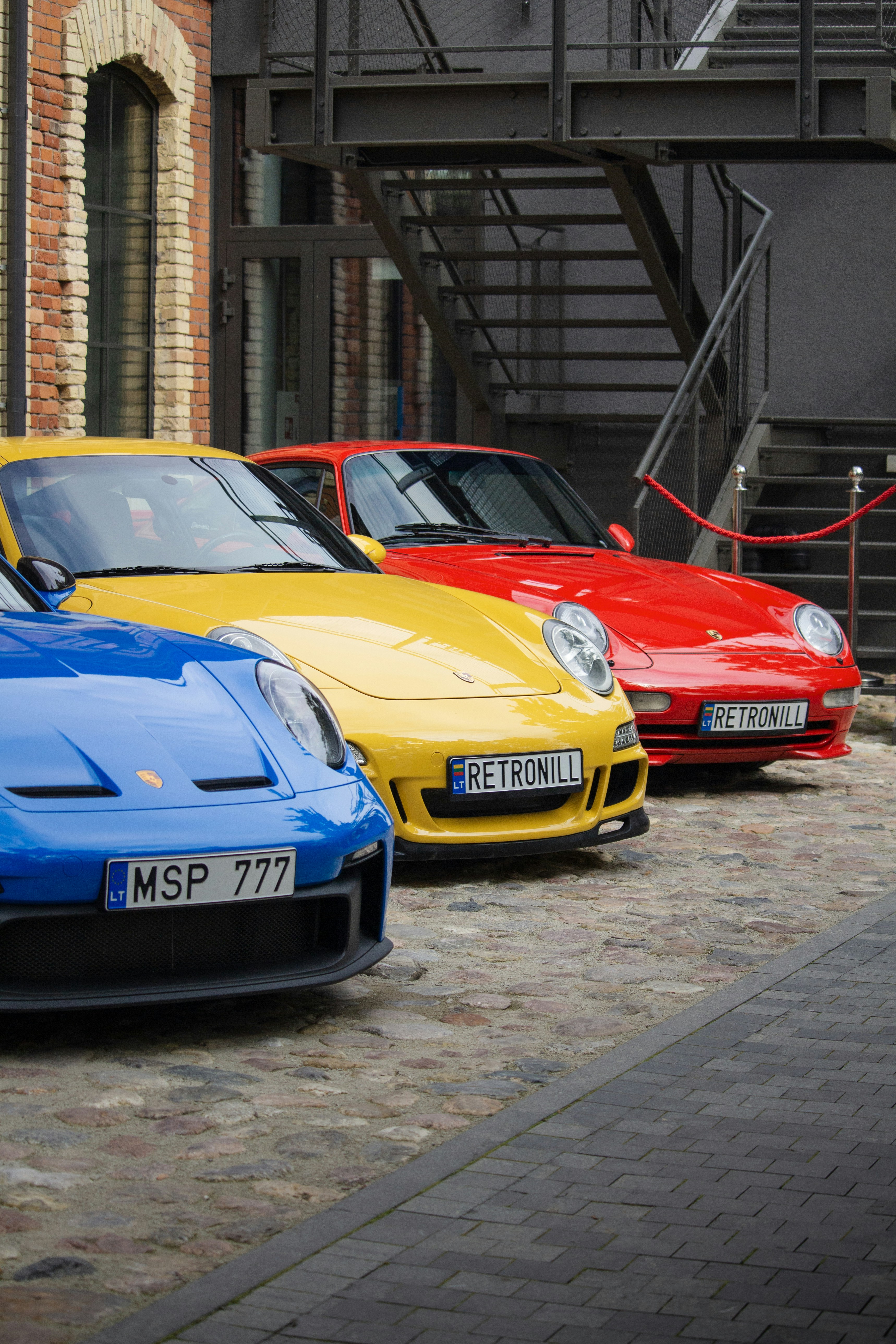 Three colorful porsche cars parked side by side