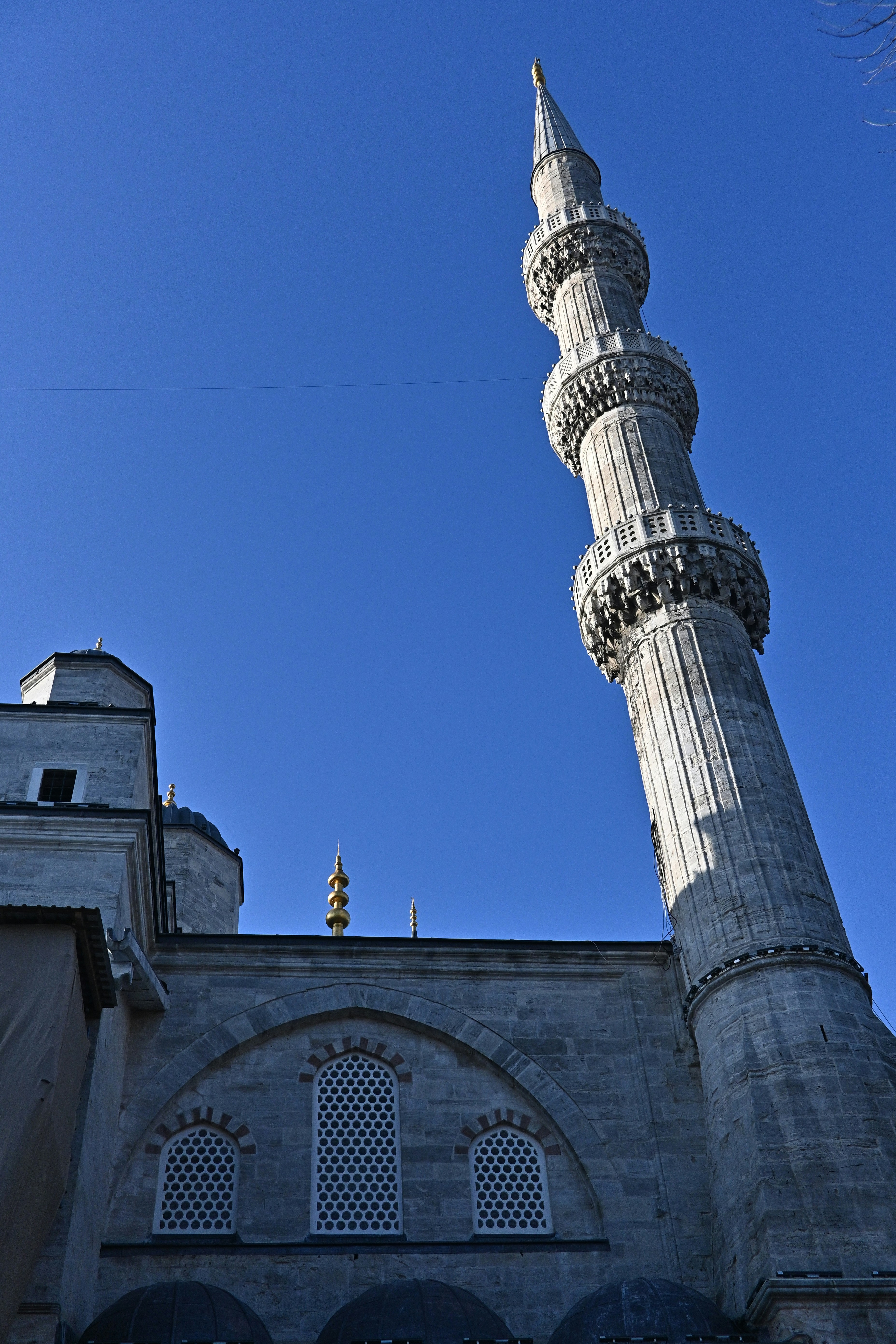 Tall minaret rises from the historic mosque, framed by a clear blue sky. Architectural details highlight the intricate design and craftsmanship.