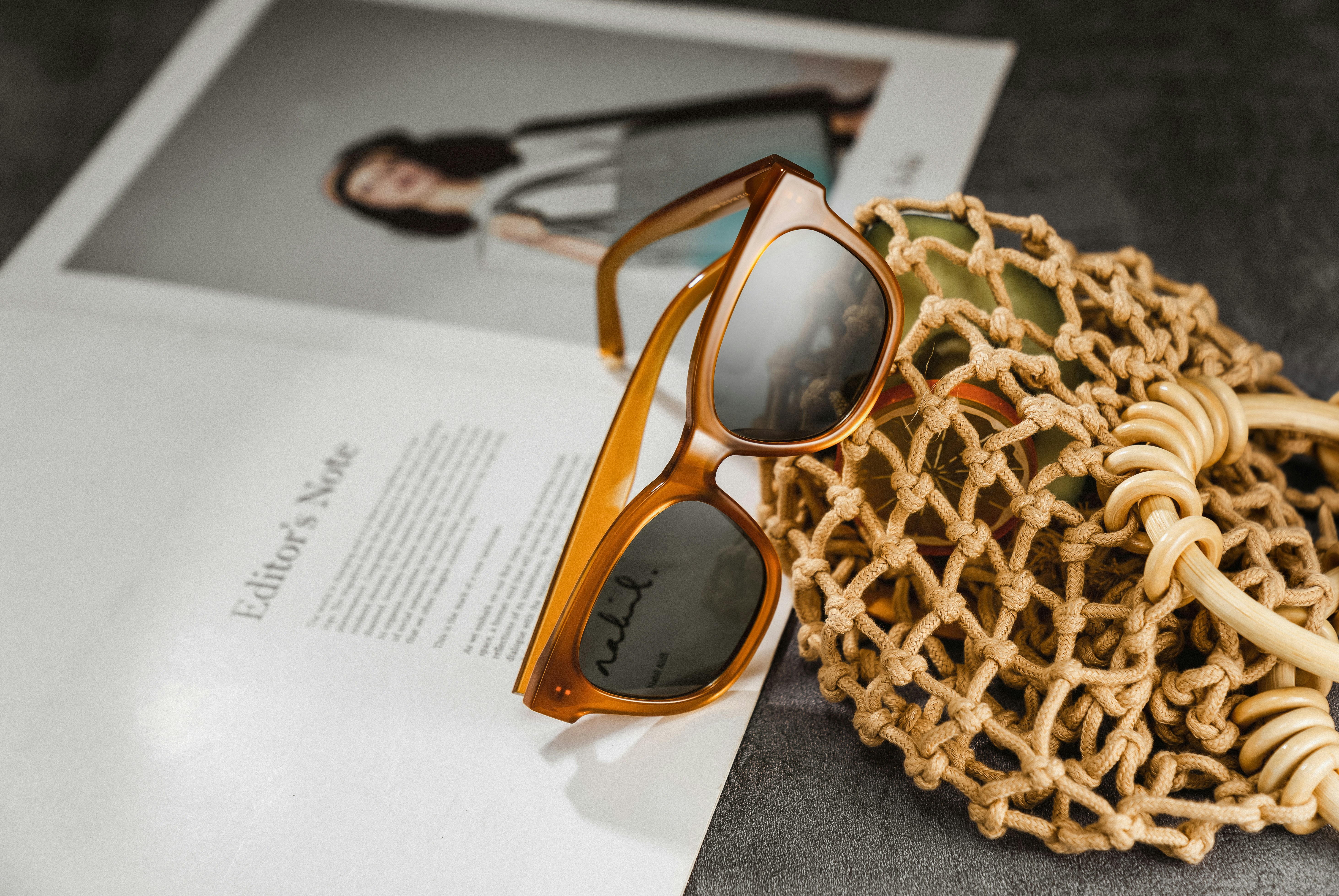 ZEELLOOL’s amber oversized sunglasses paired with a woven bag and fashion magazine, creating an effortless resort-style fashion moment. | Sunglasses resting on an open magazine page.