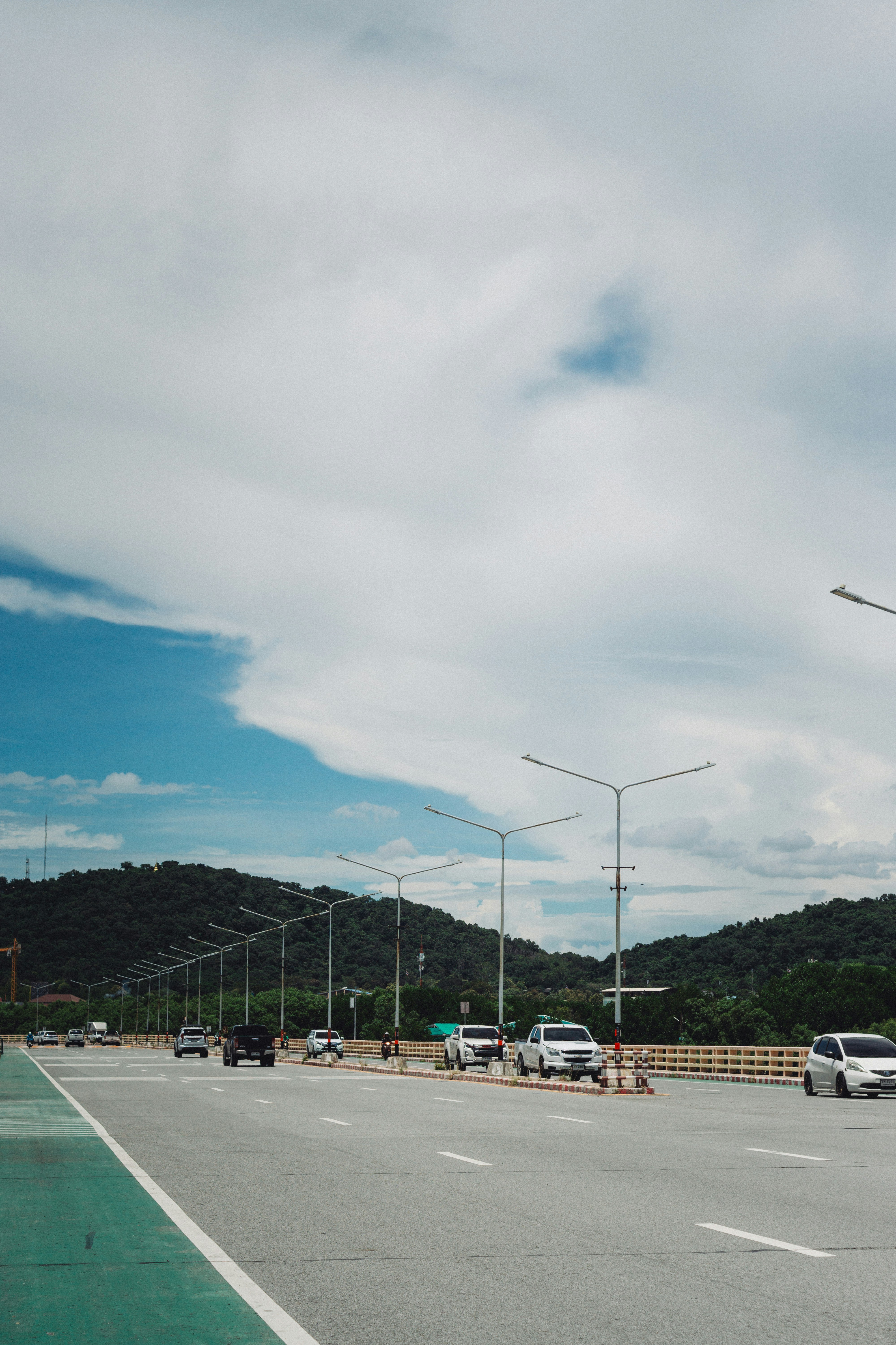 Cars drive on a highway with distant mountains and clouds.