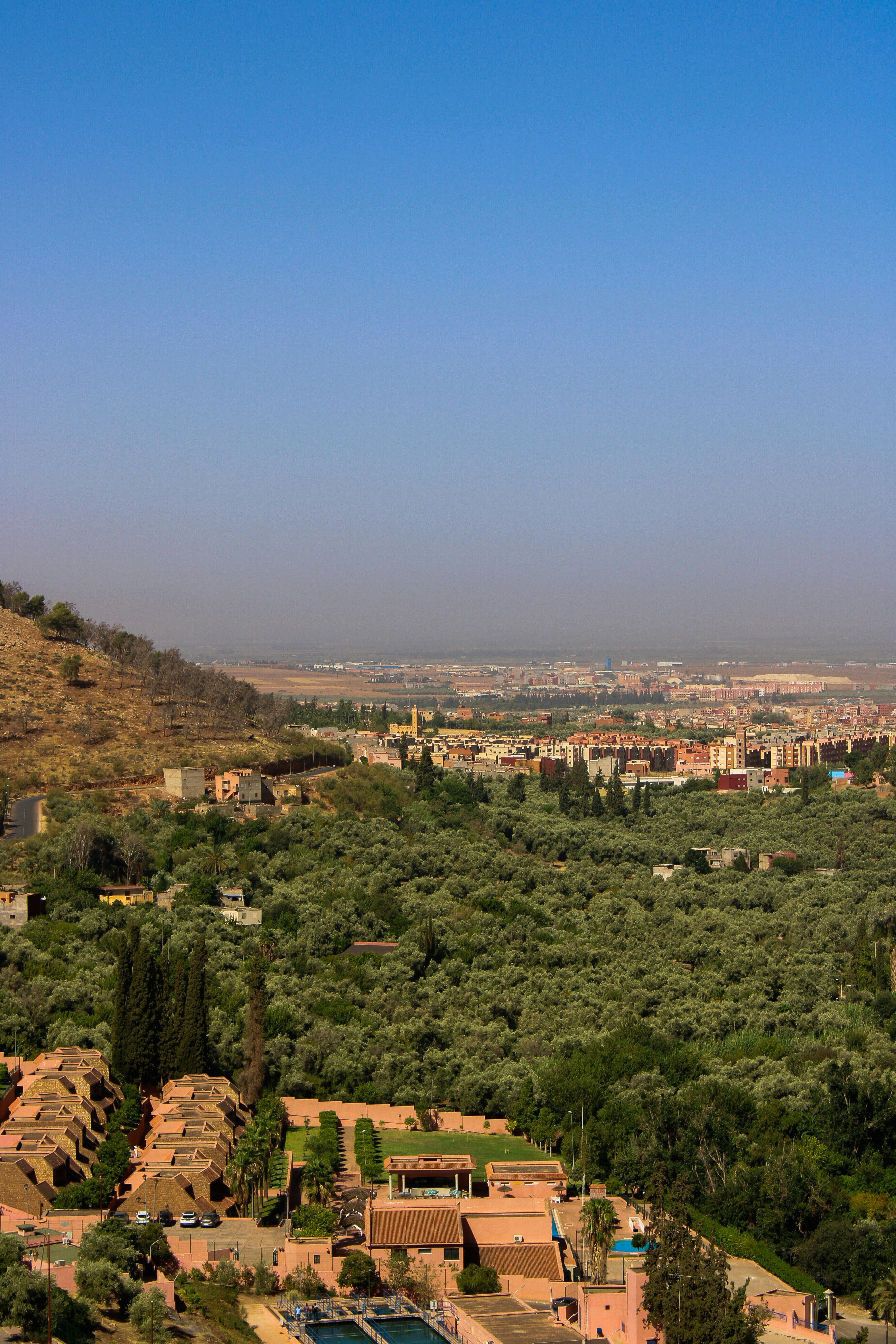 Green valley with buildings and distant city under blue sky