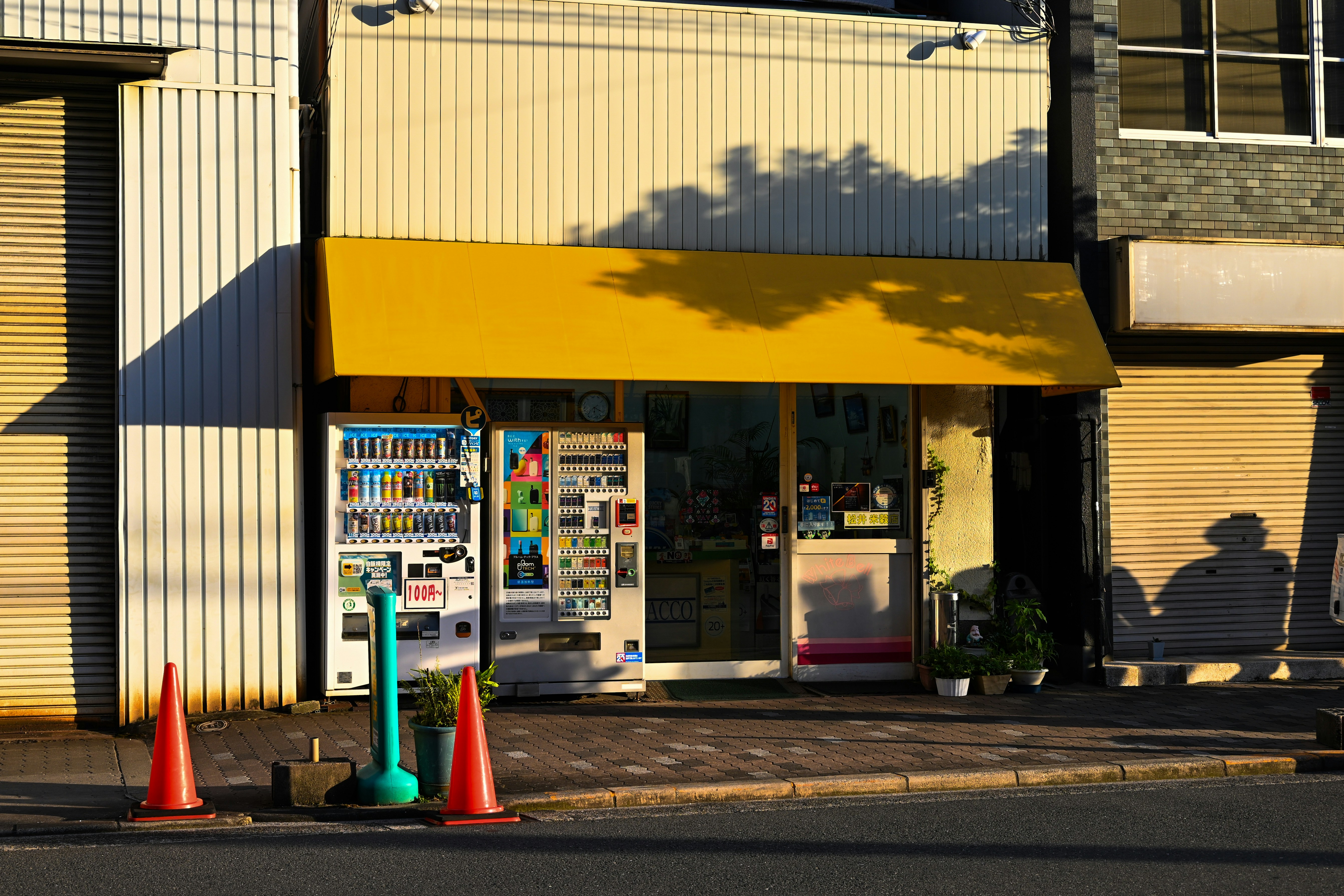 Corner store with yellow awning and vending machines.
