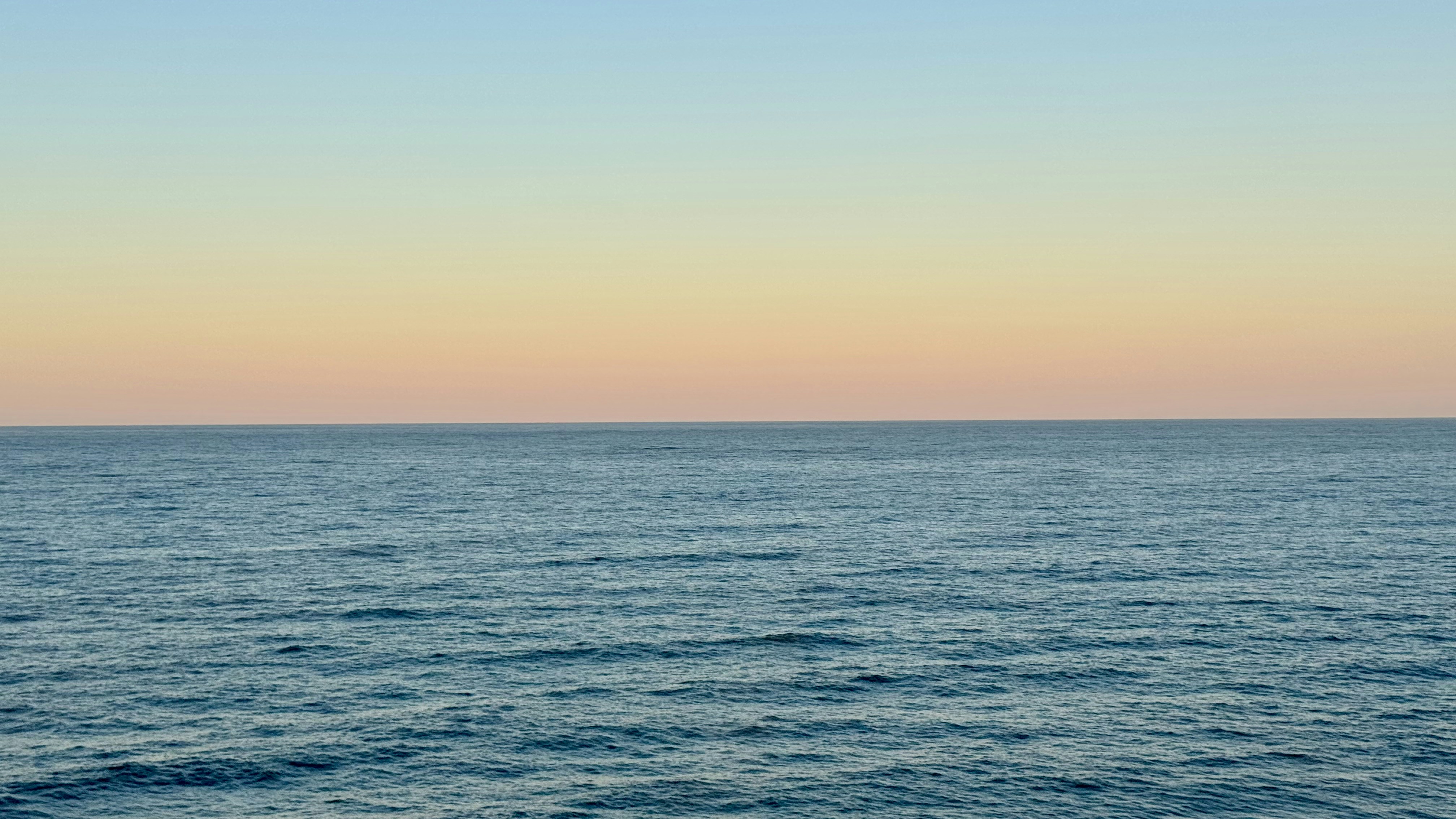 Calm ocean waves stretch toward a pastel horizon, blending serene blues and soft pinks. The tranquil scene invites reflection.