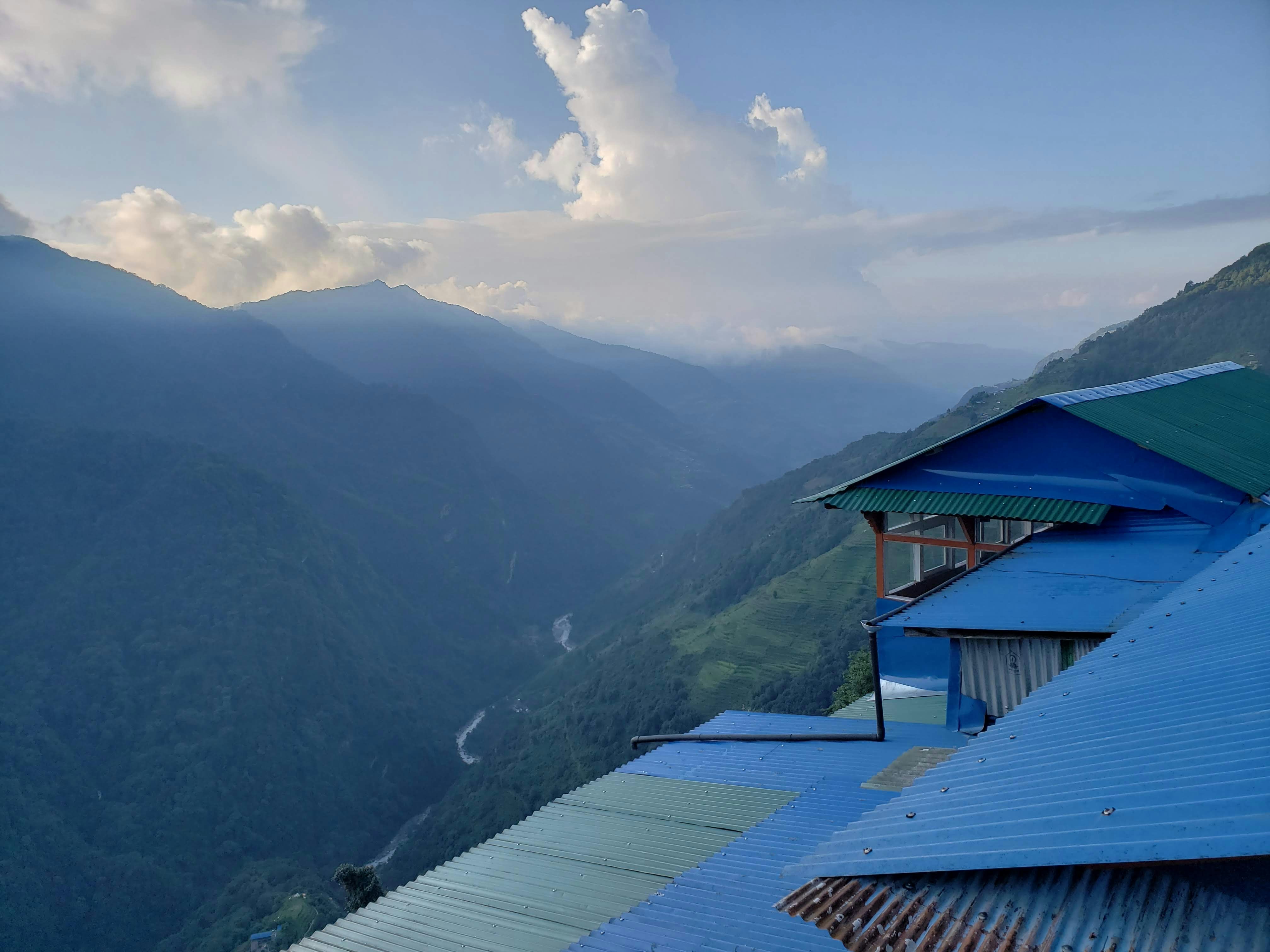 View from a tea house high up in the Himalayas | Blue roofs overlook misty mountains and a winding river.