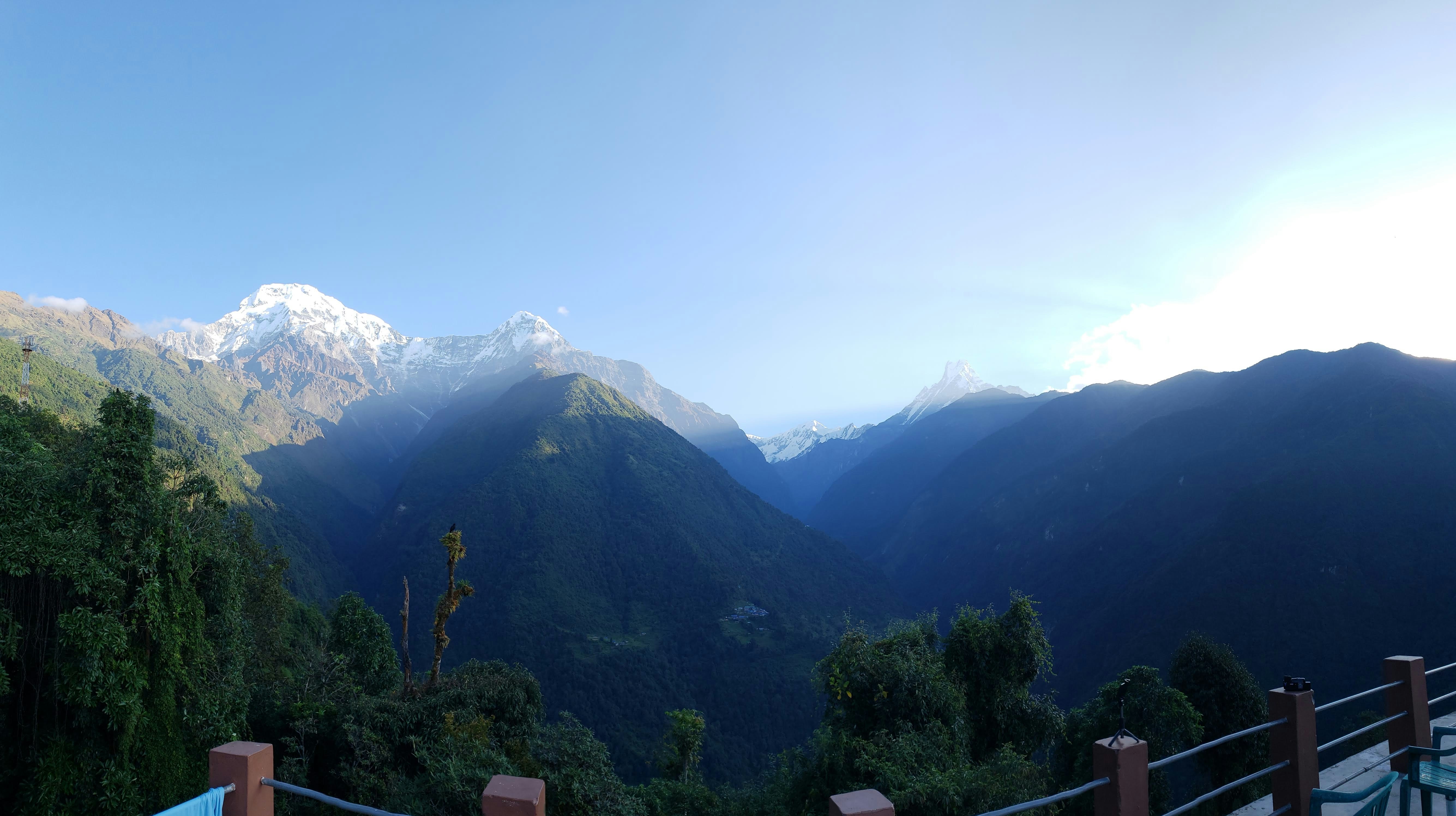 View from a tea house high up in the Himalayas | Snow-capped mountains rise above a lush green valley.