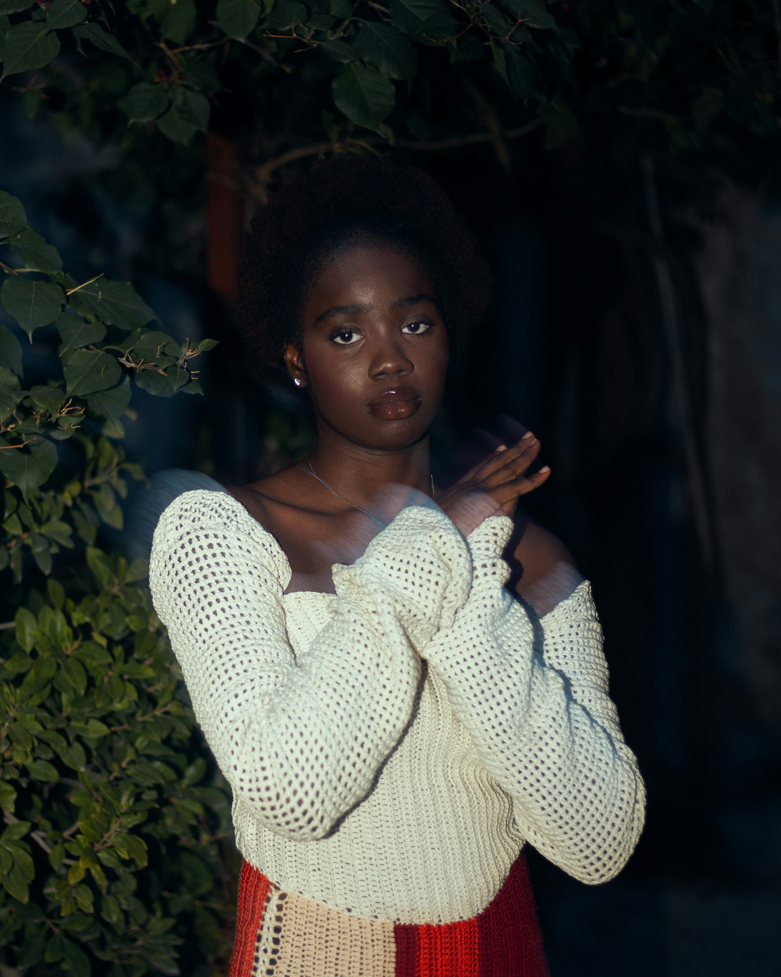 Young woman with dark curly hair wearing a white sweater.