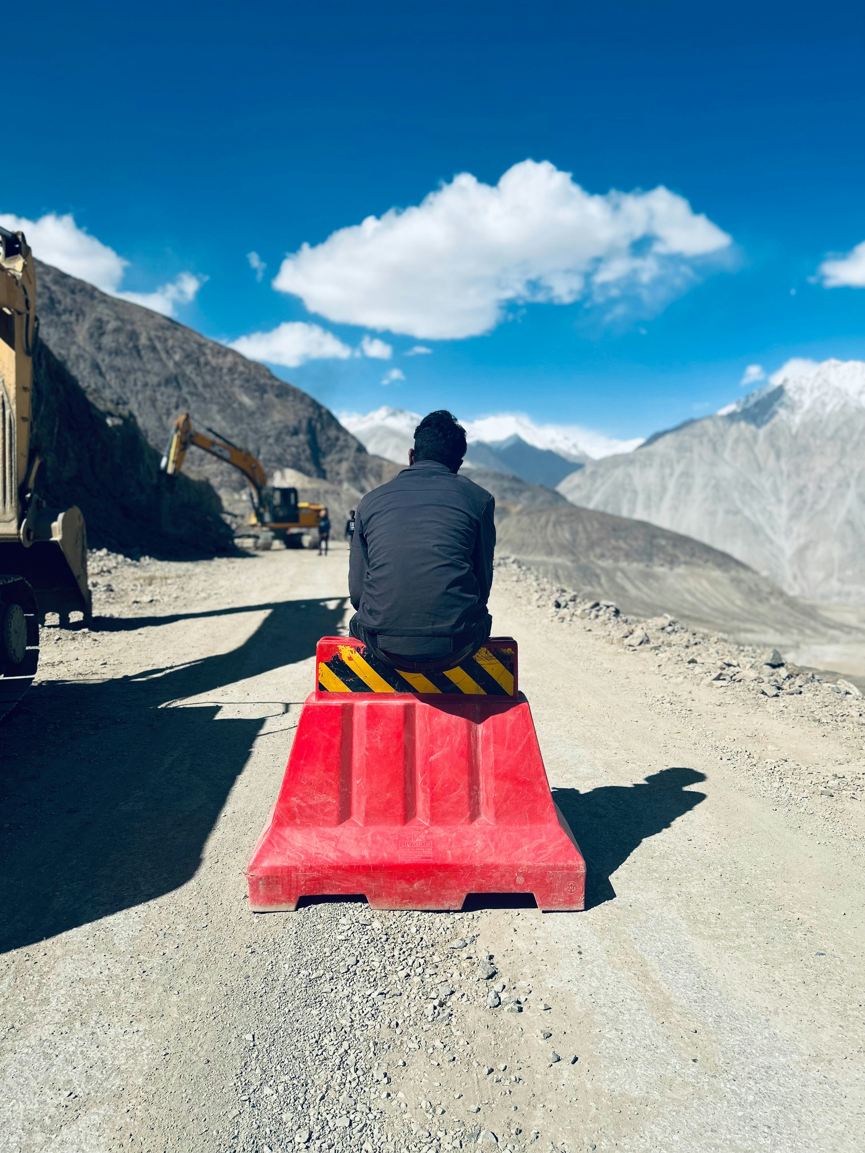 Man sits on barrier overlooking mountainous construction site