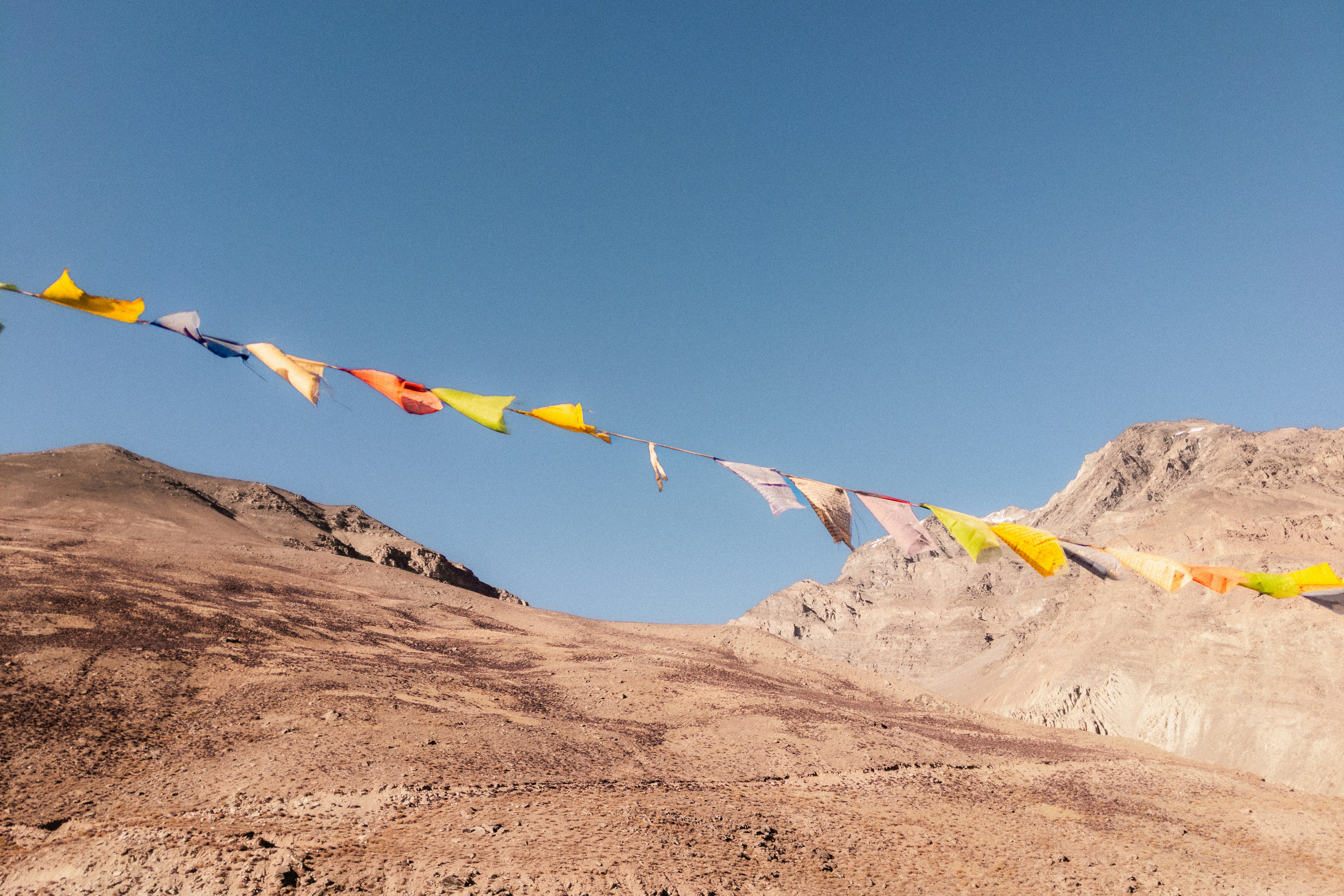 Colorful prayer flags flutter against a clear blue sky.