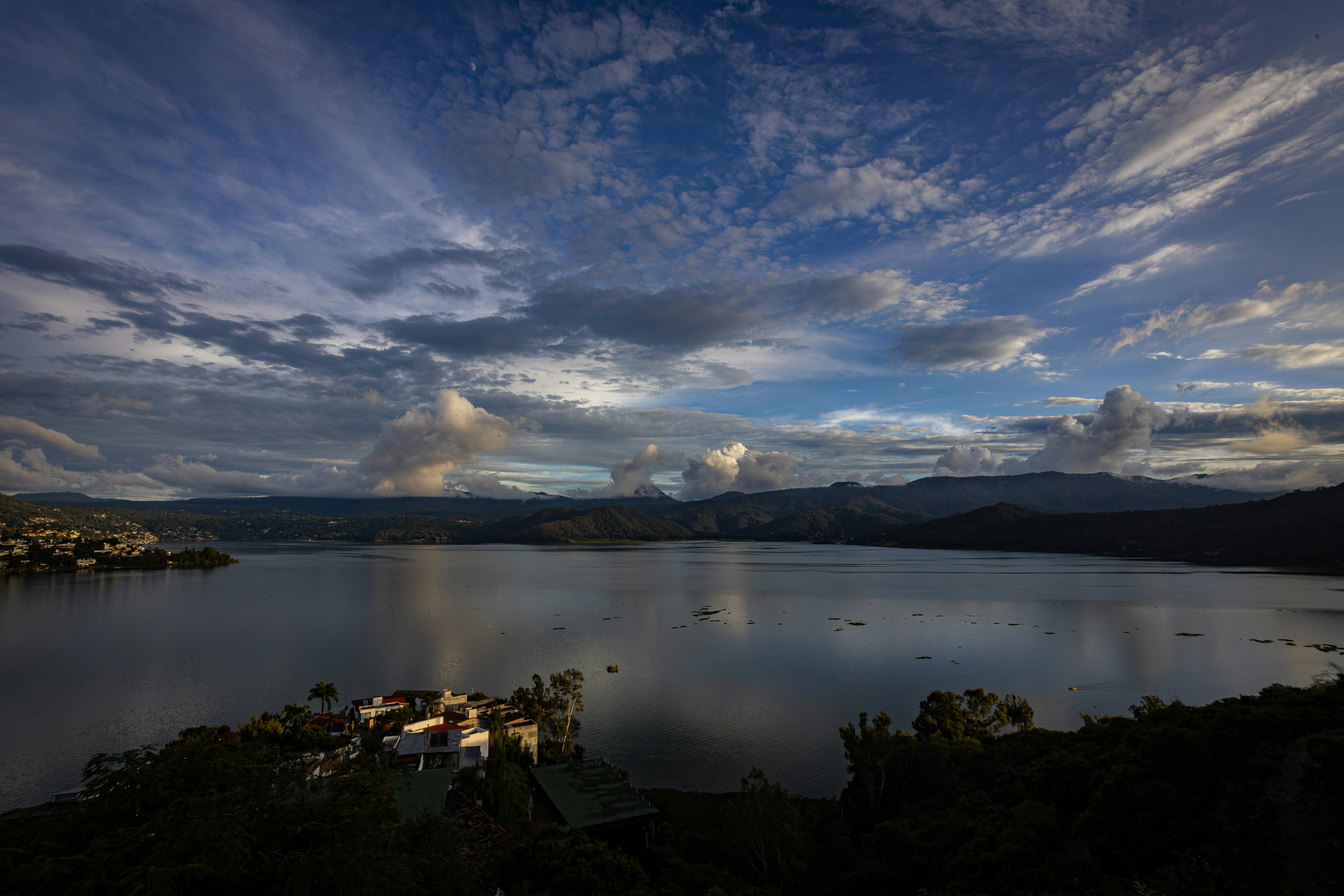 Calm lake surrounded by hills under a dramatic sky.