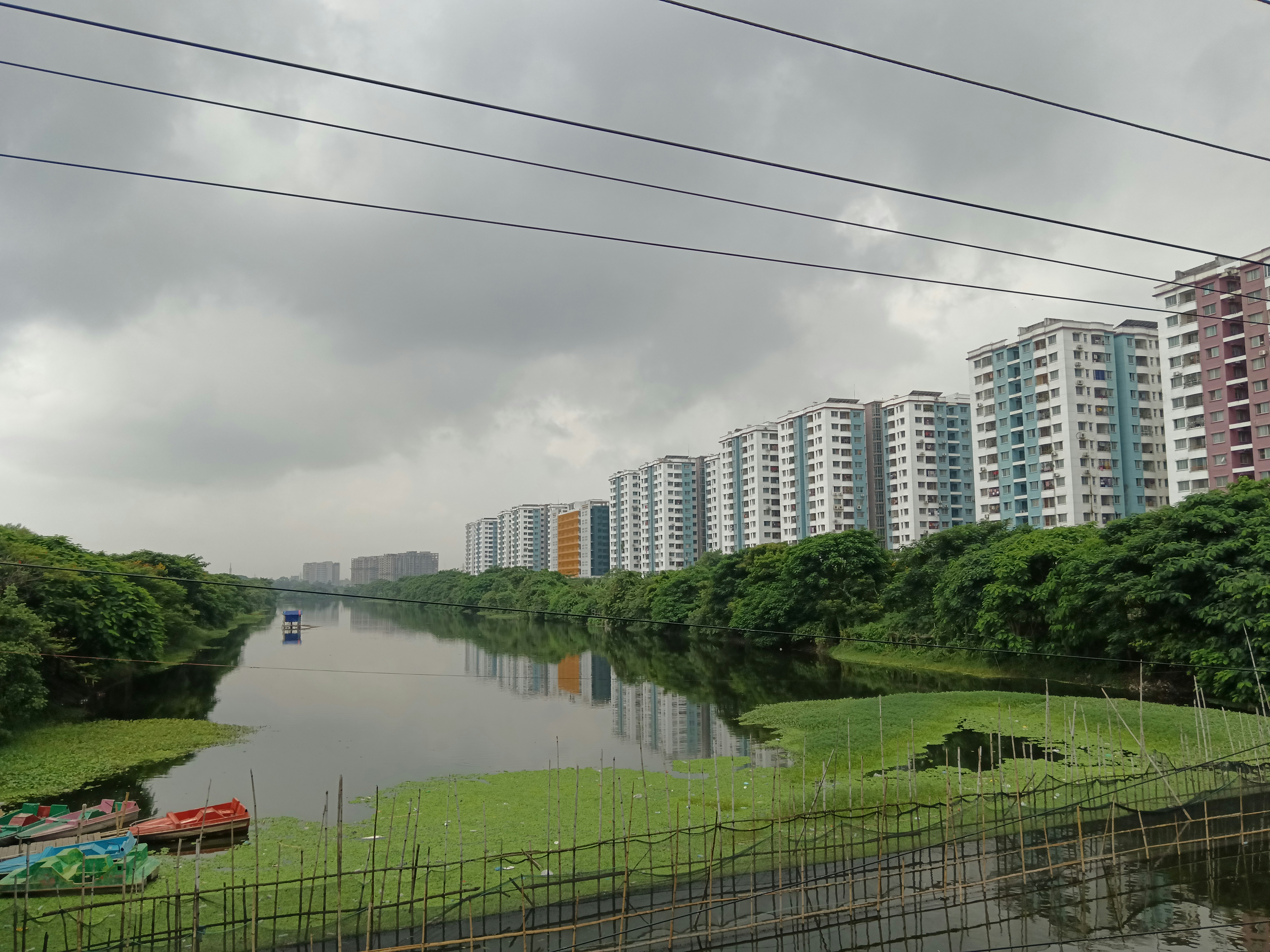 Apartment buildings line a calm river under cloudy skies.