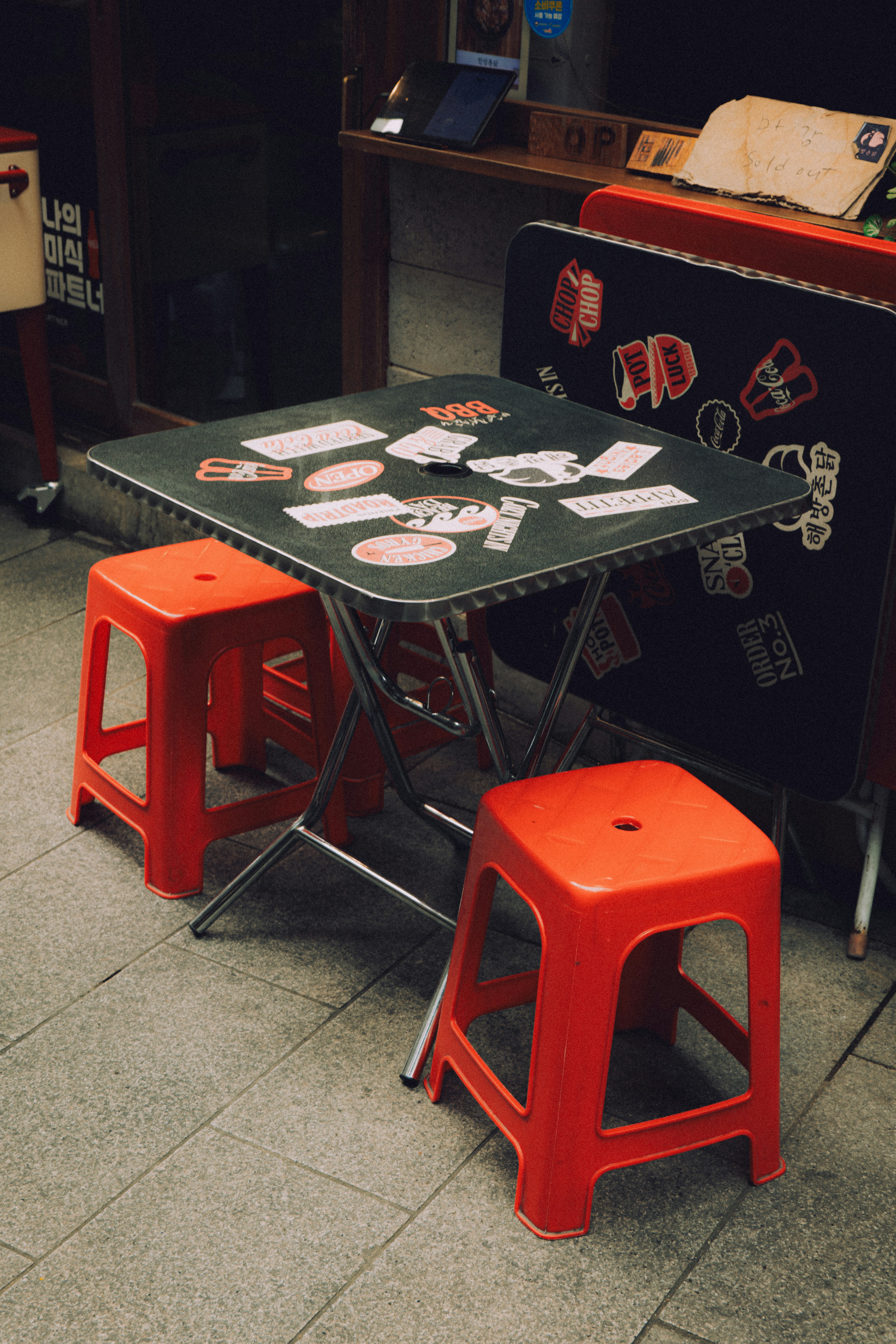 Table with two red stools outside a building. photo – Free Street ...