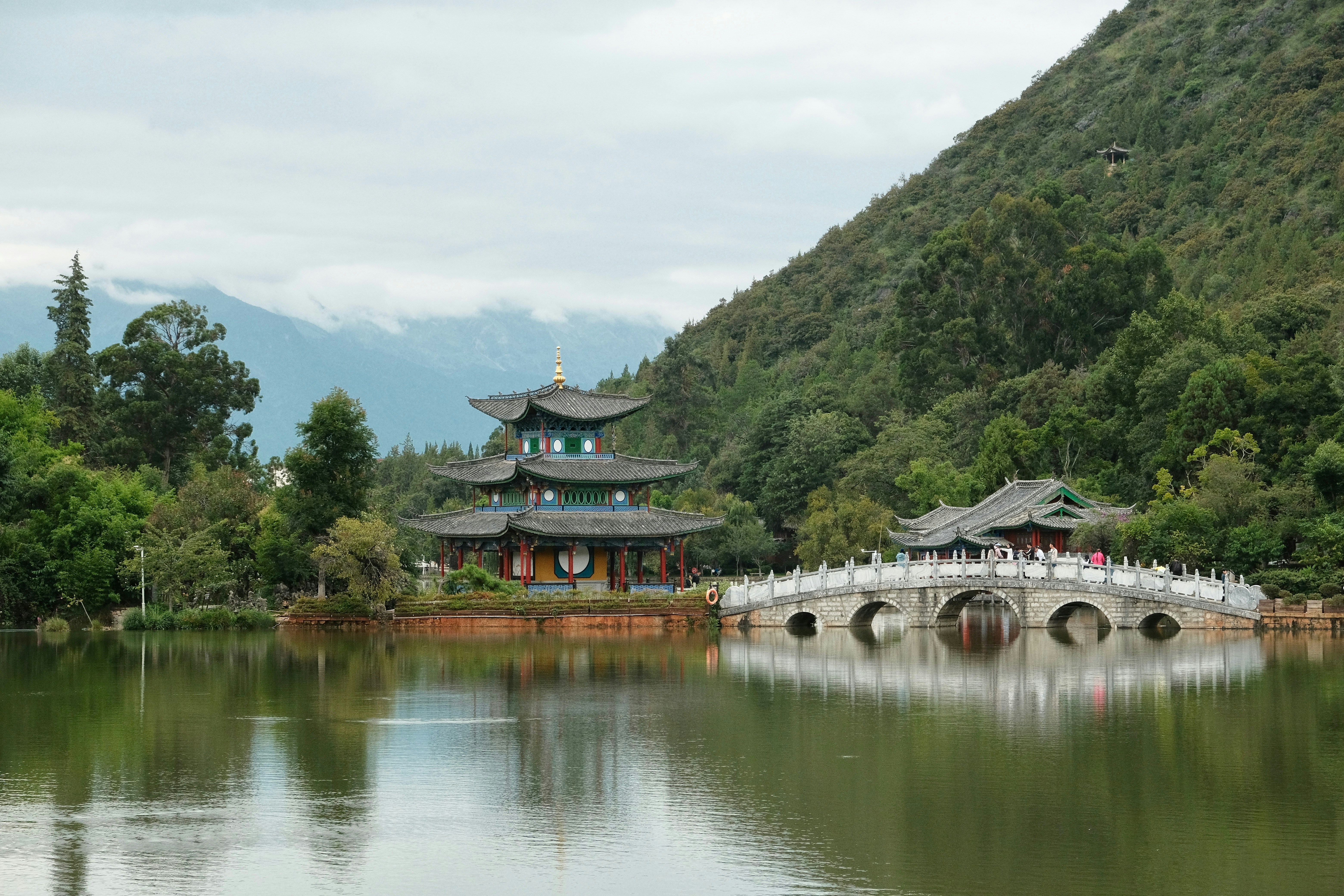 Traditional chinese temple by a lake with a bridge.