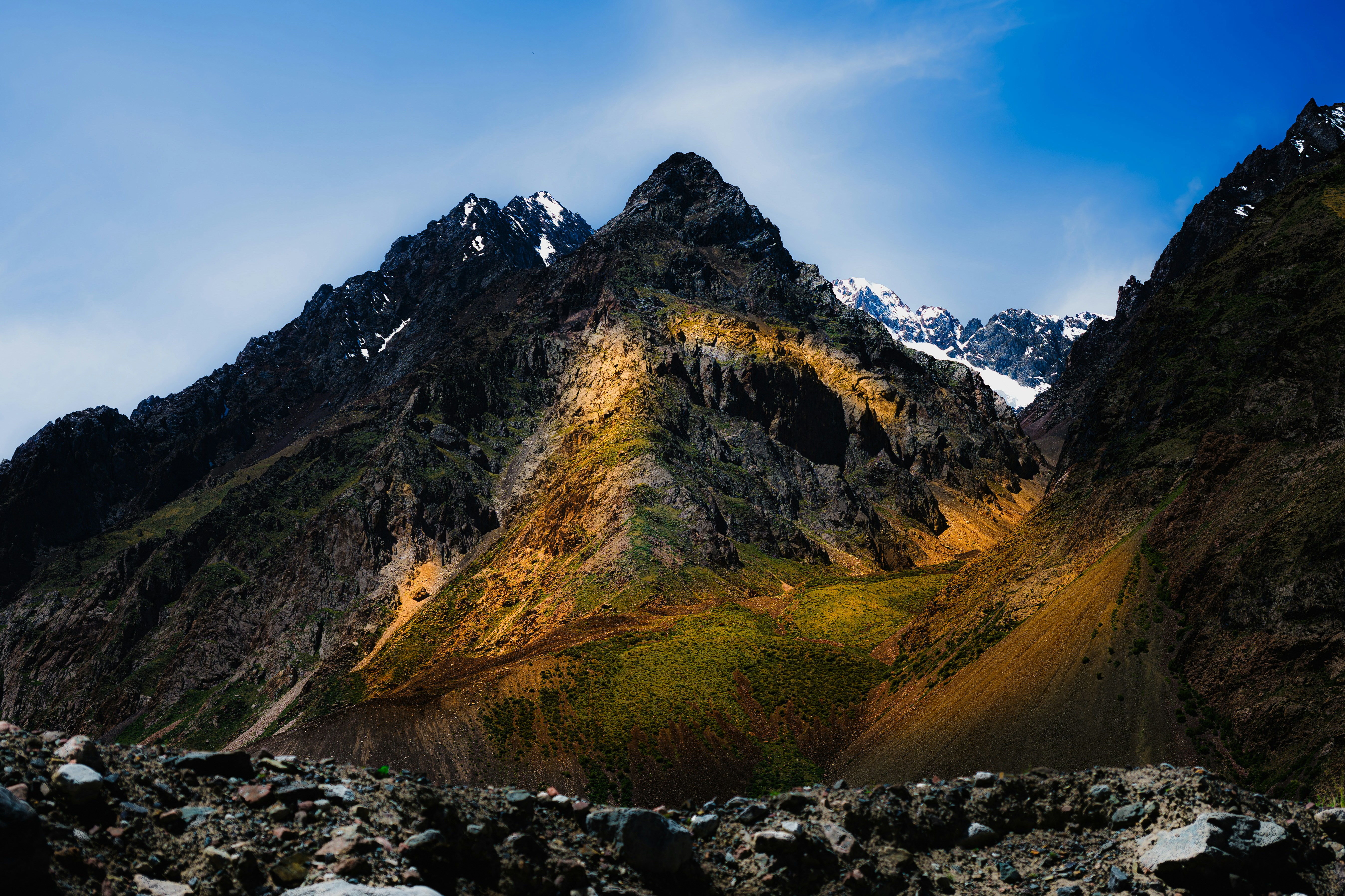 Sunlight illuminates a rugged mountain slope under a blue sky.